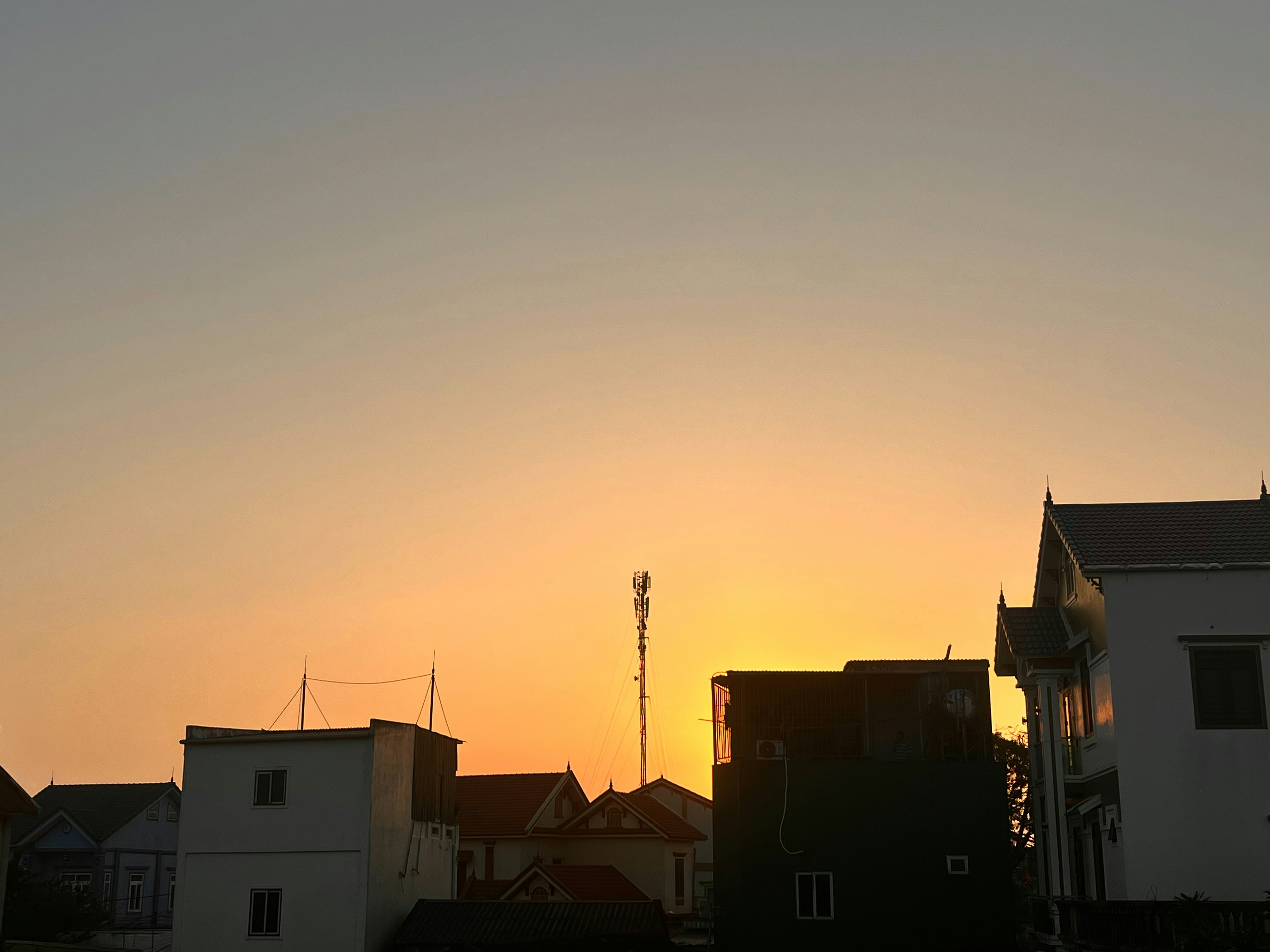 Dusk Over Suburb: Rooftops Framing a Quiet Sunset with a Central Mast