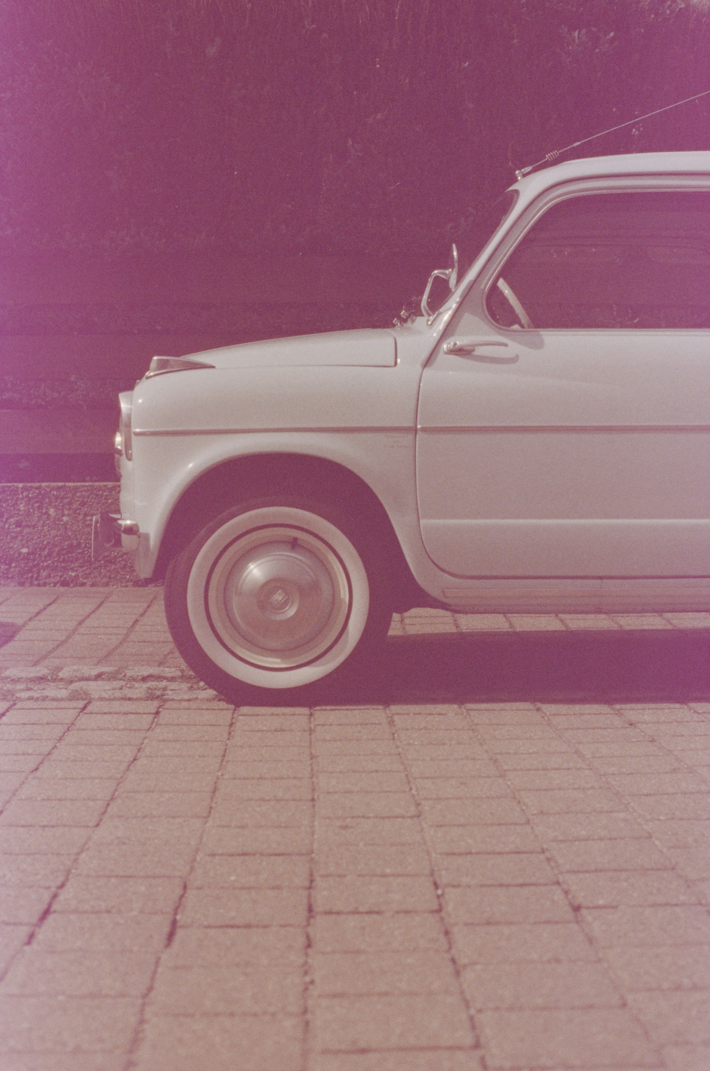 Side view of a vintage Fiat 500 on a cobblestone path with a pinkish tint.
