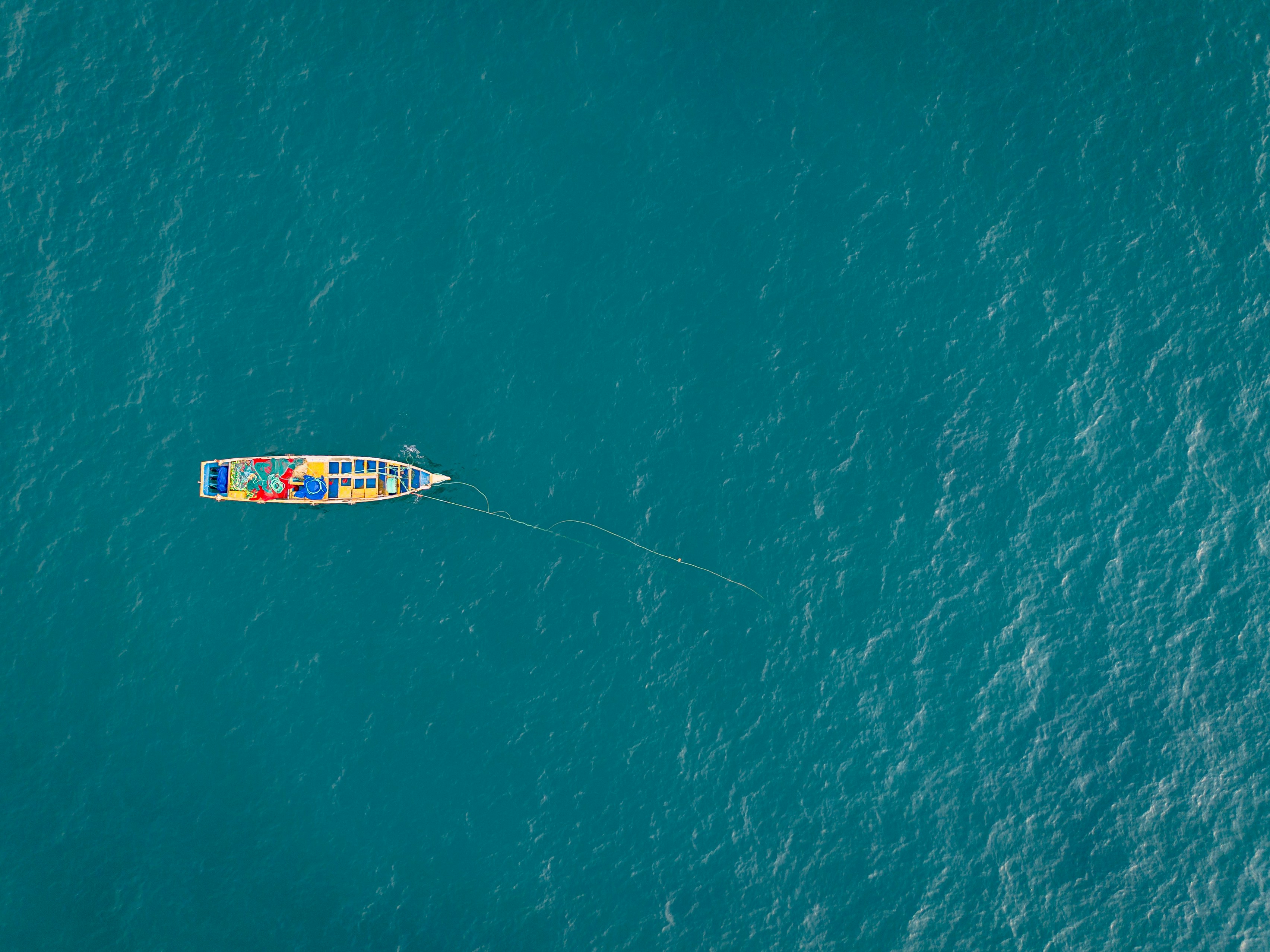 Cerulean Drift: Aerial Portrait of a Tiny Vessel in Open Water
