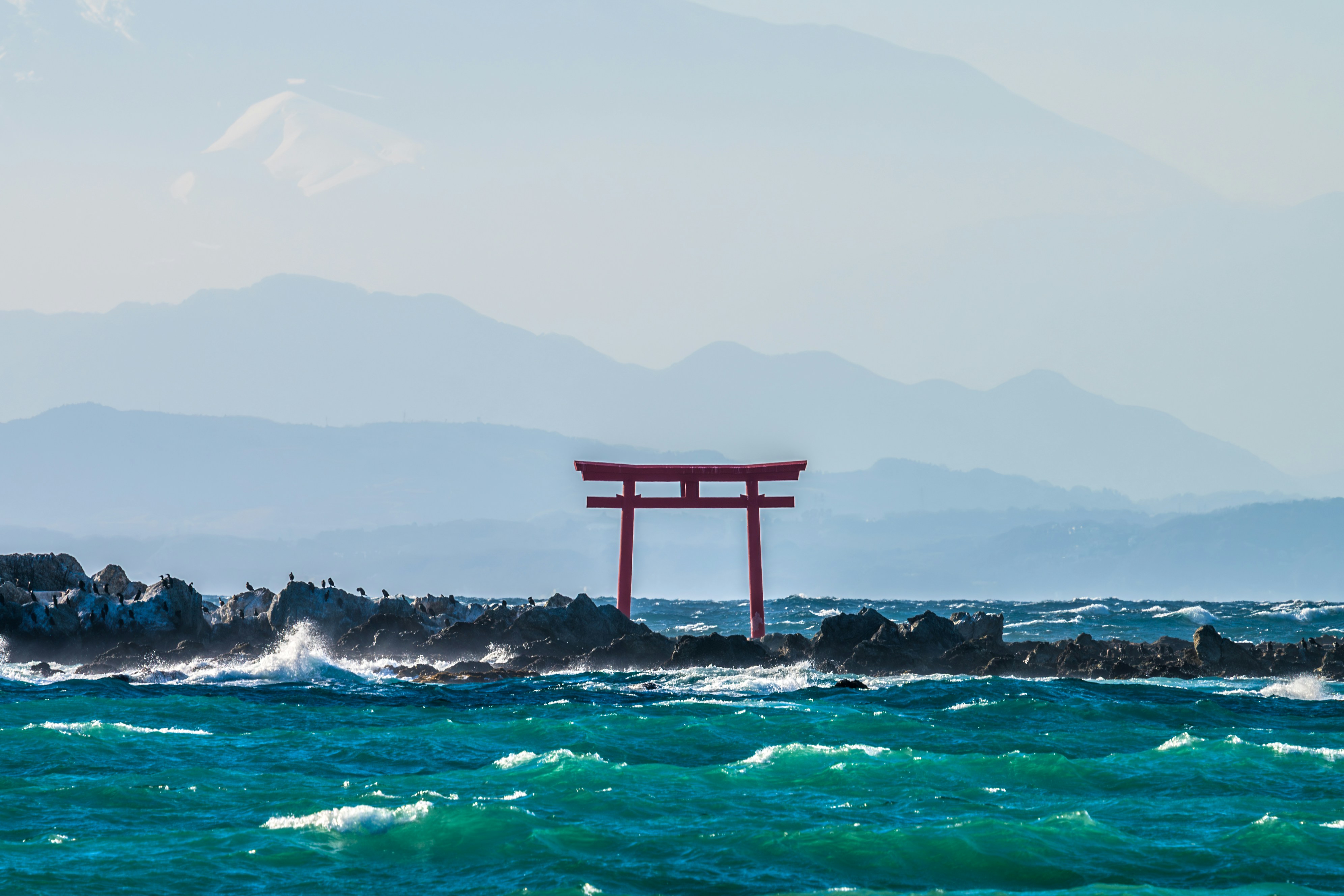 Torii gate stands on rocks in the ocean. | a large body of water with a red structure in the middle of it