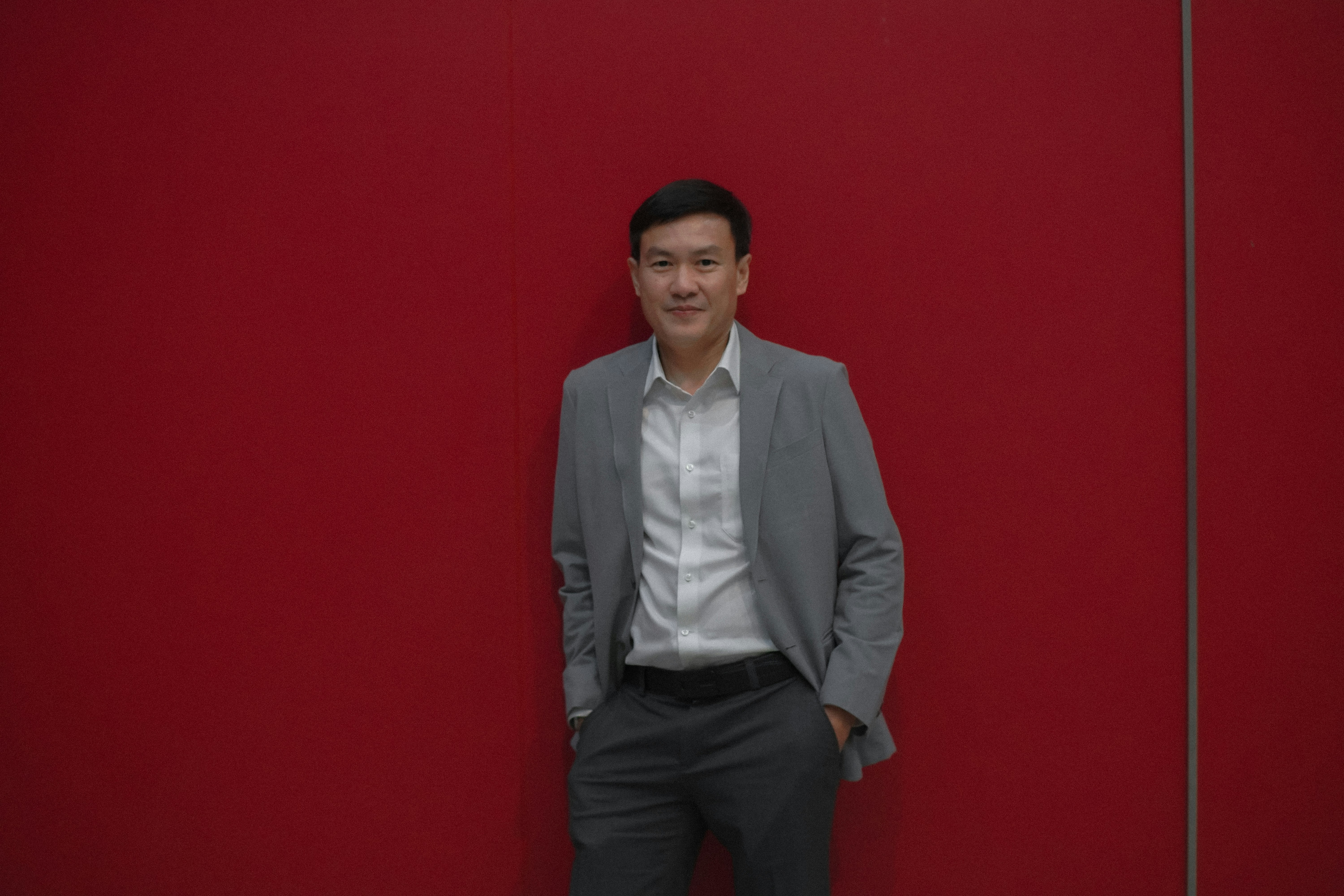 Man in a gray suit standing against a bold red backdrop.