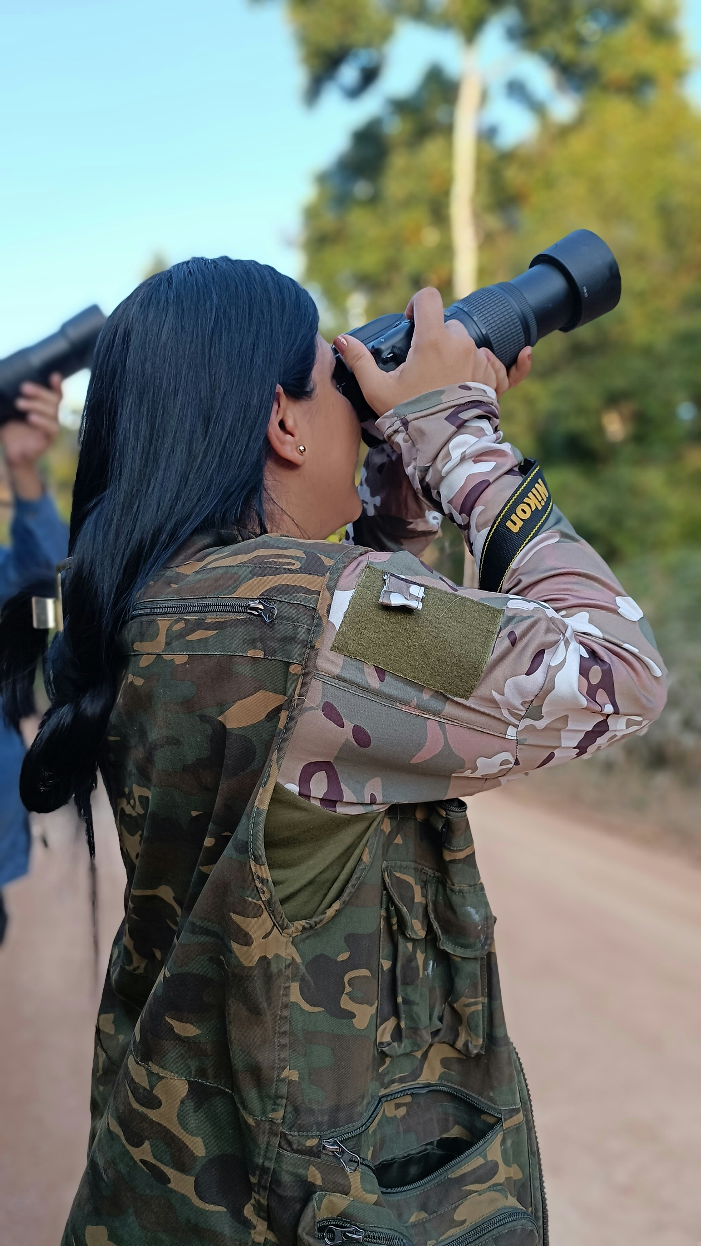 Cameraperson in camouflage takes a high-angle shot with a telephoto lens, capturing a moment of focus and action outdoors. This is a candid, likely documentary-style scene.