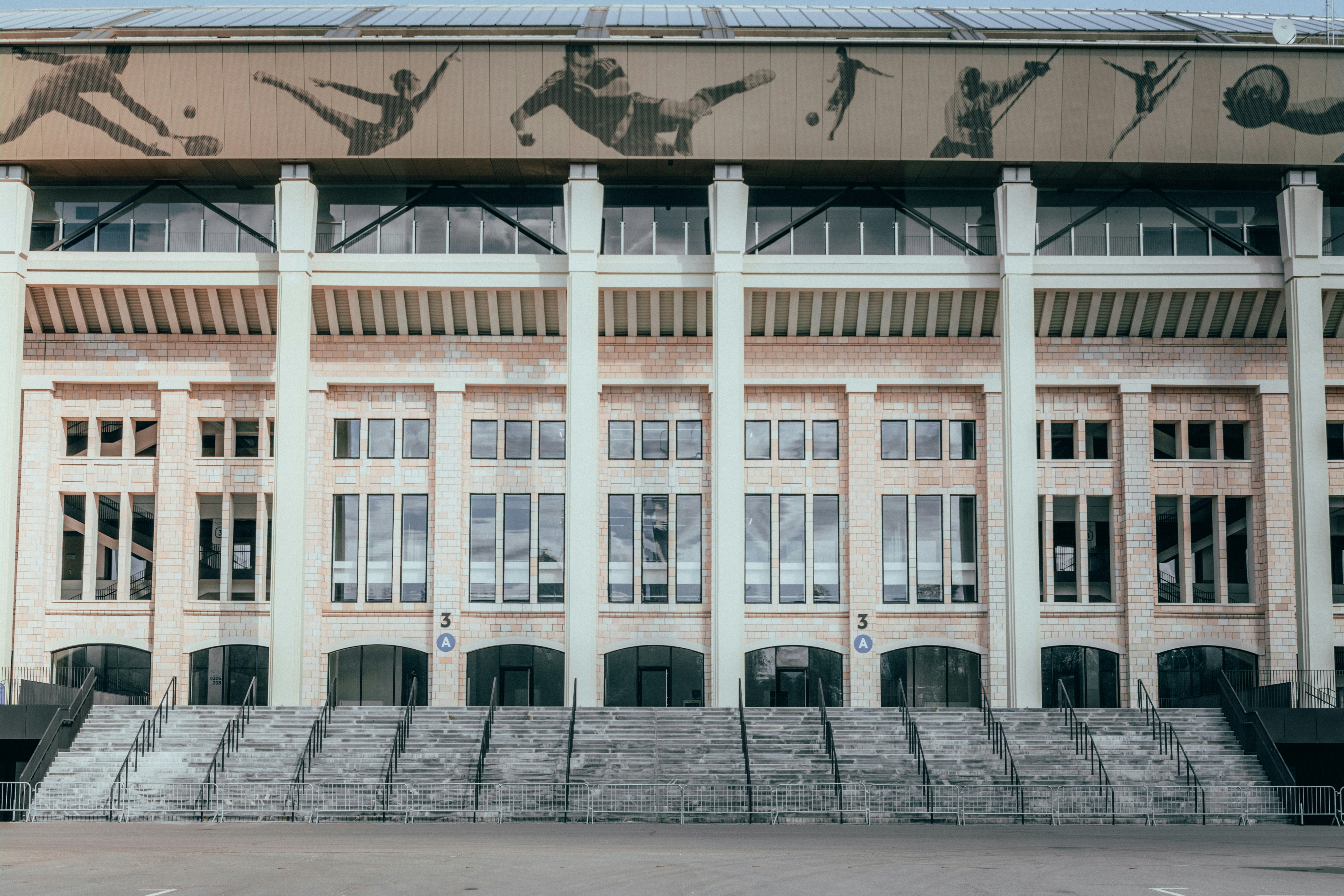 Front view of Luzhniki Stadium entrance showcasing a blend of contemporary and classical architectural elements with sports silhouettes above.