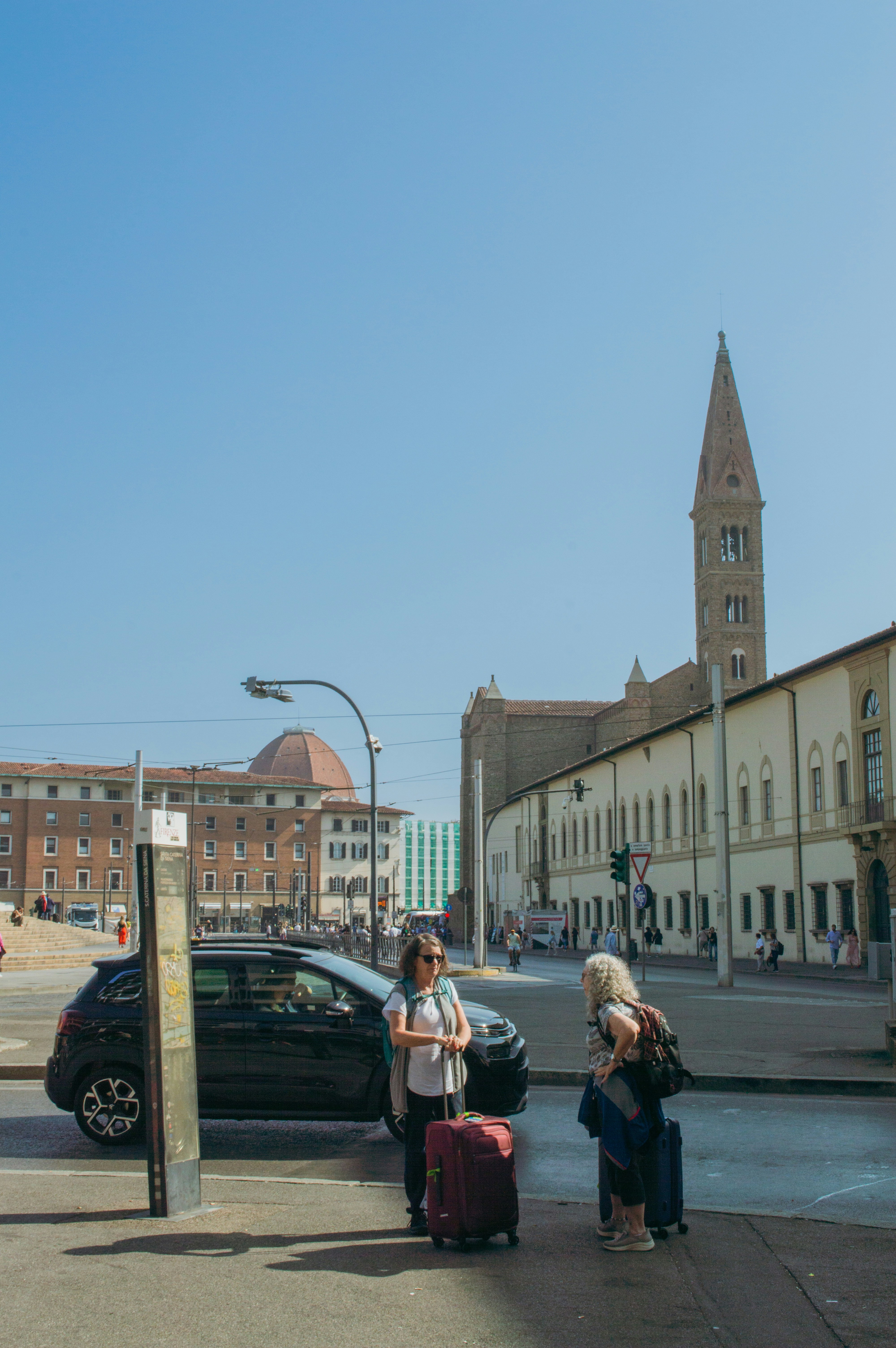 Sunlit Street Scene: Two Travelers Pause with Luggage Before a Church Tower