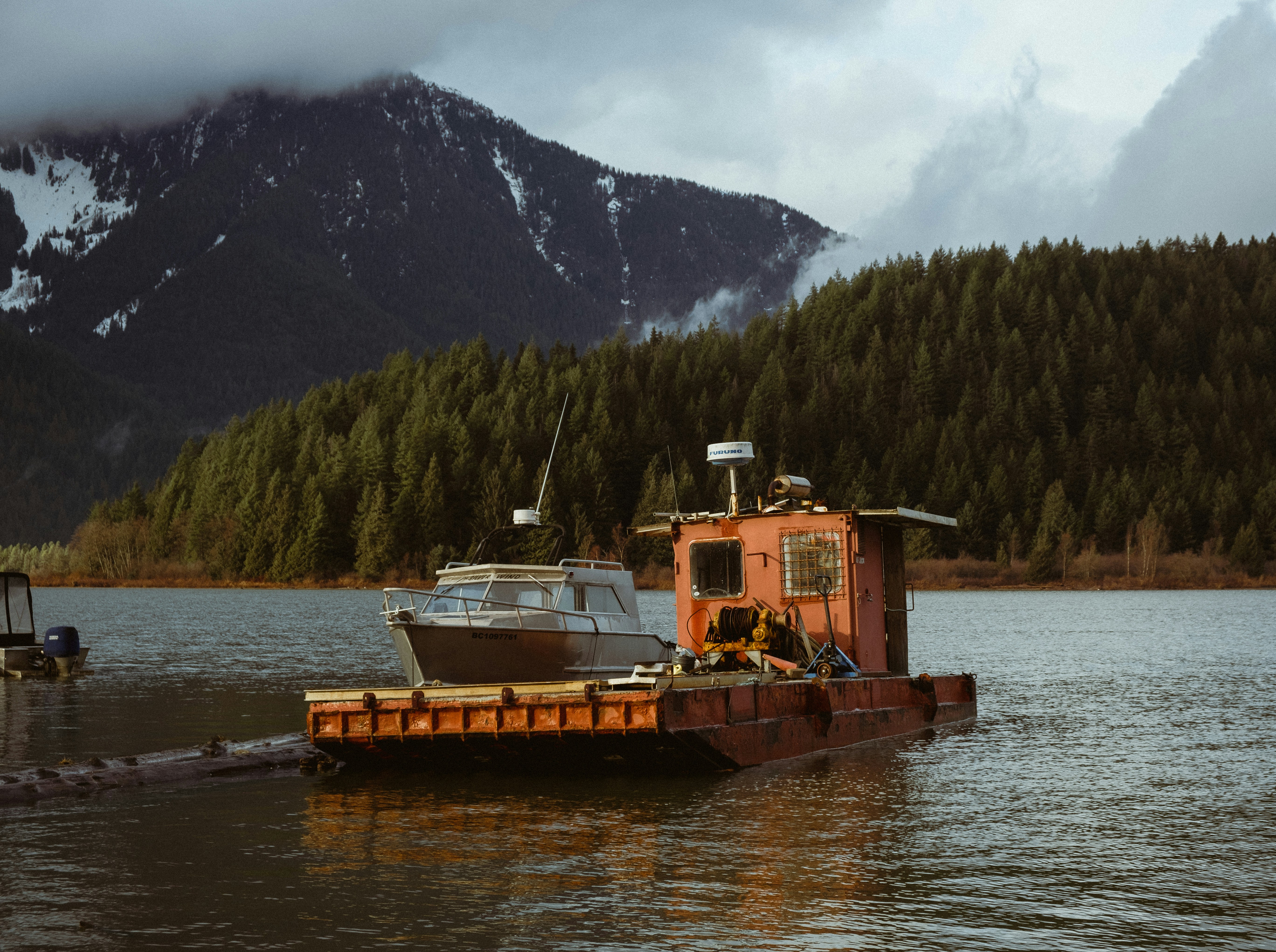 A boat rests on calm waters with a backdrop of towering mountains under a cloudy sky.