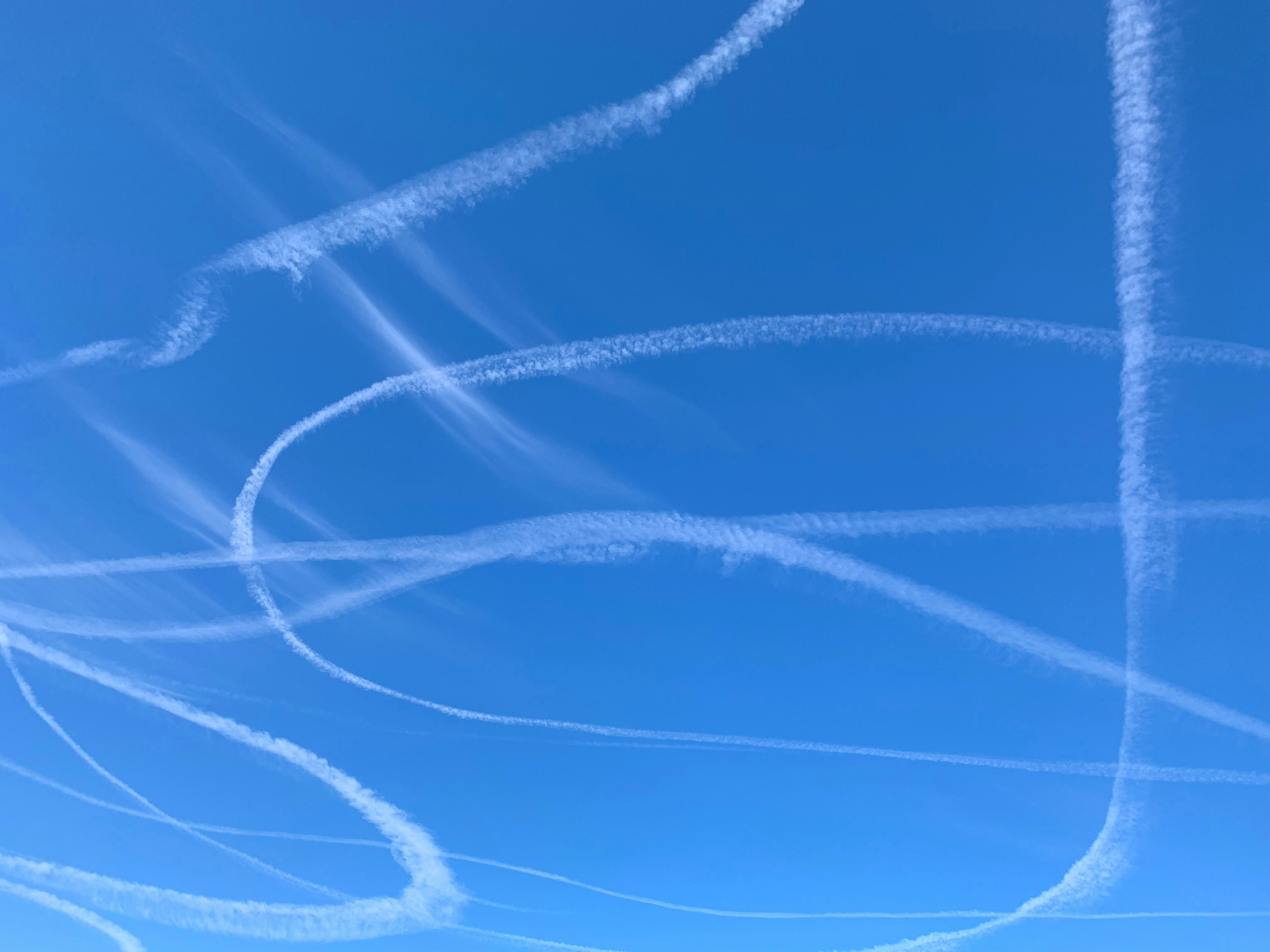 White contrails crisscross a clear blue sky in intricate patterns.