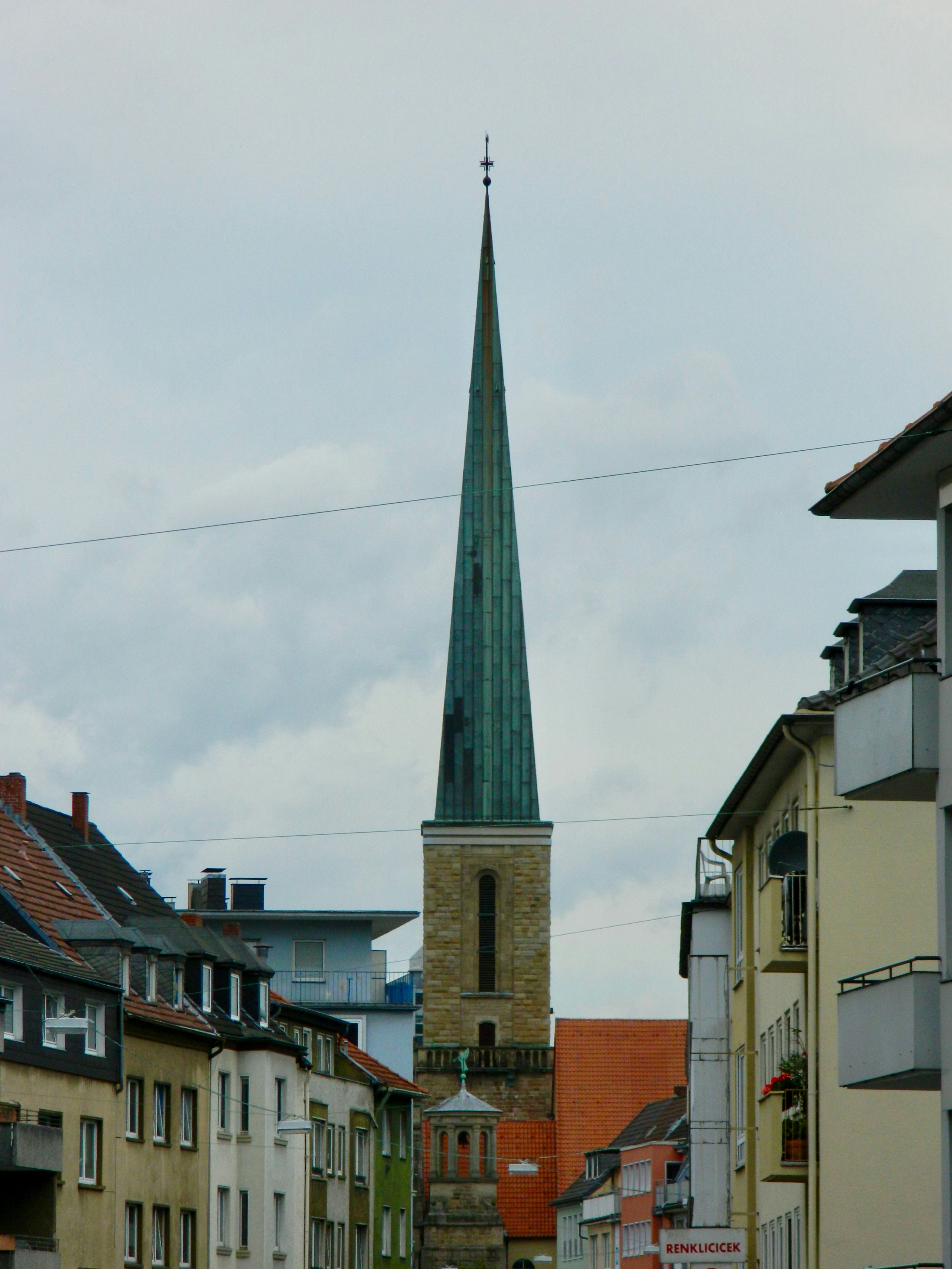 Tall church spire rises above city rooftops under a cloudy sky.