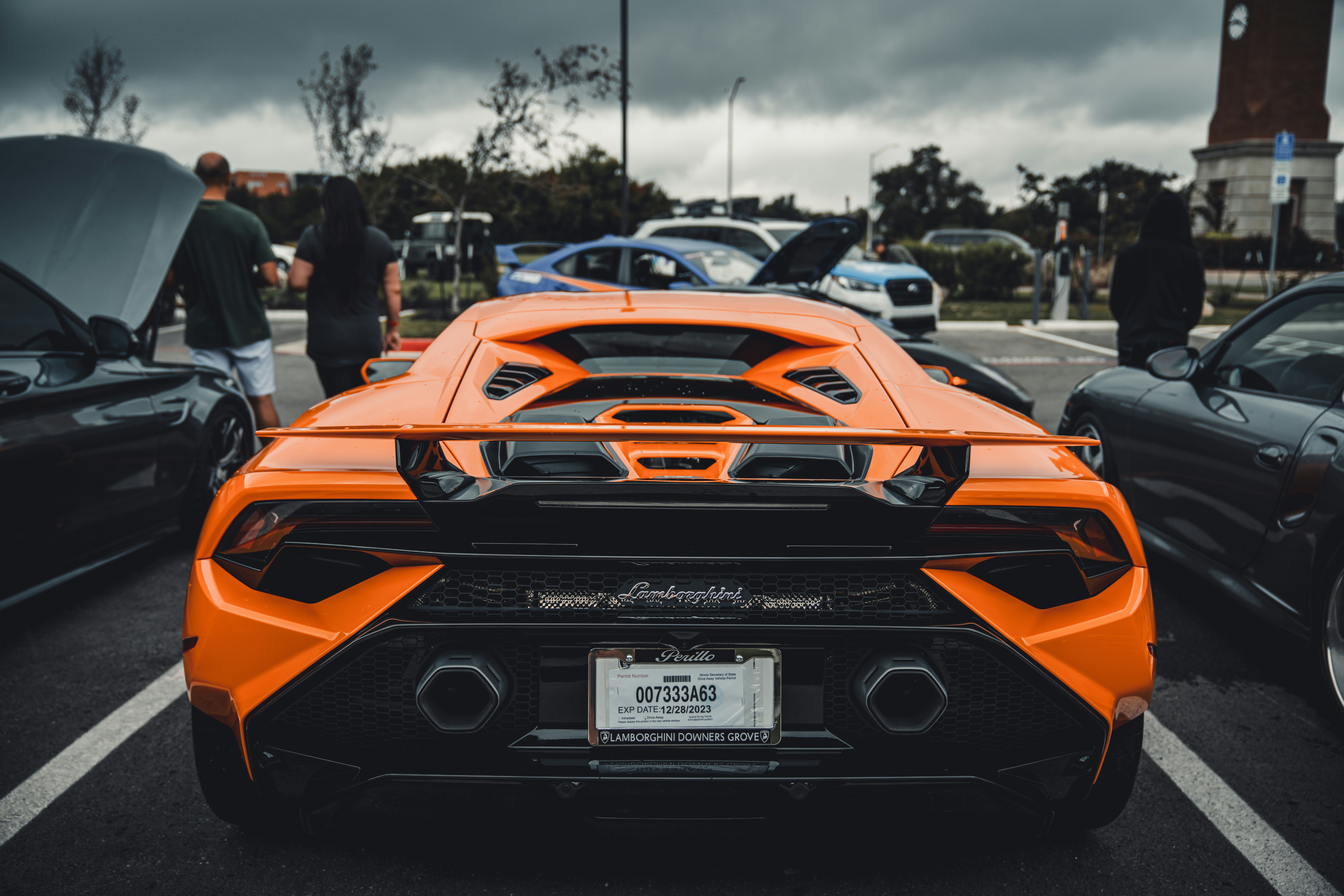 Rear view of a striking orange Lamborghini parked among other luxury cars, showcasing its aerodynamic design and distinctive features.
