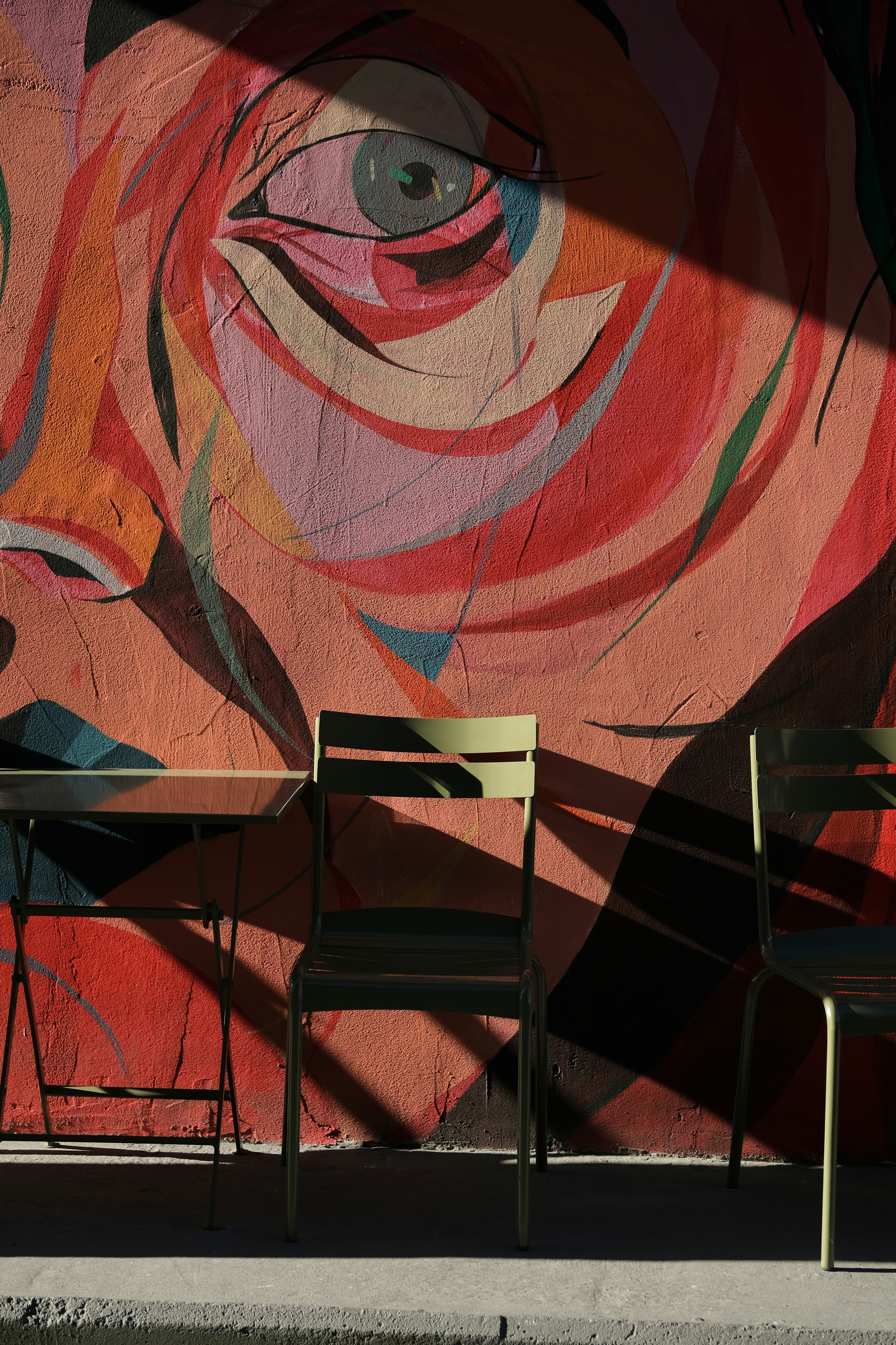 Chromatic Gaze on a Sunlit Wall: A Mural with Shadowed Chairs