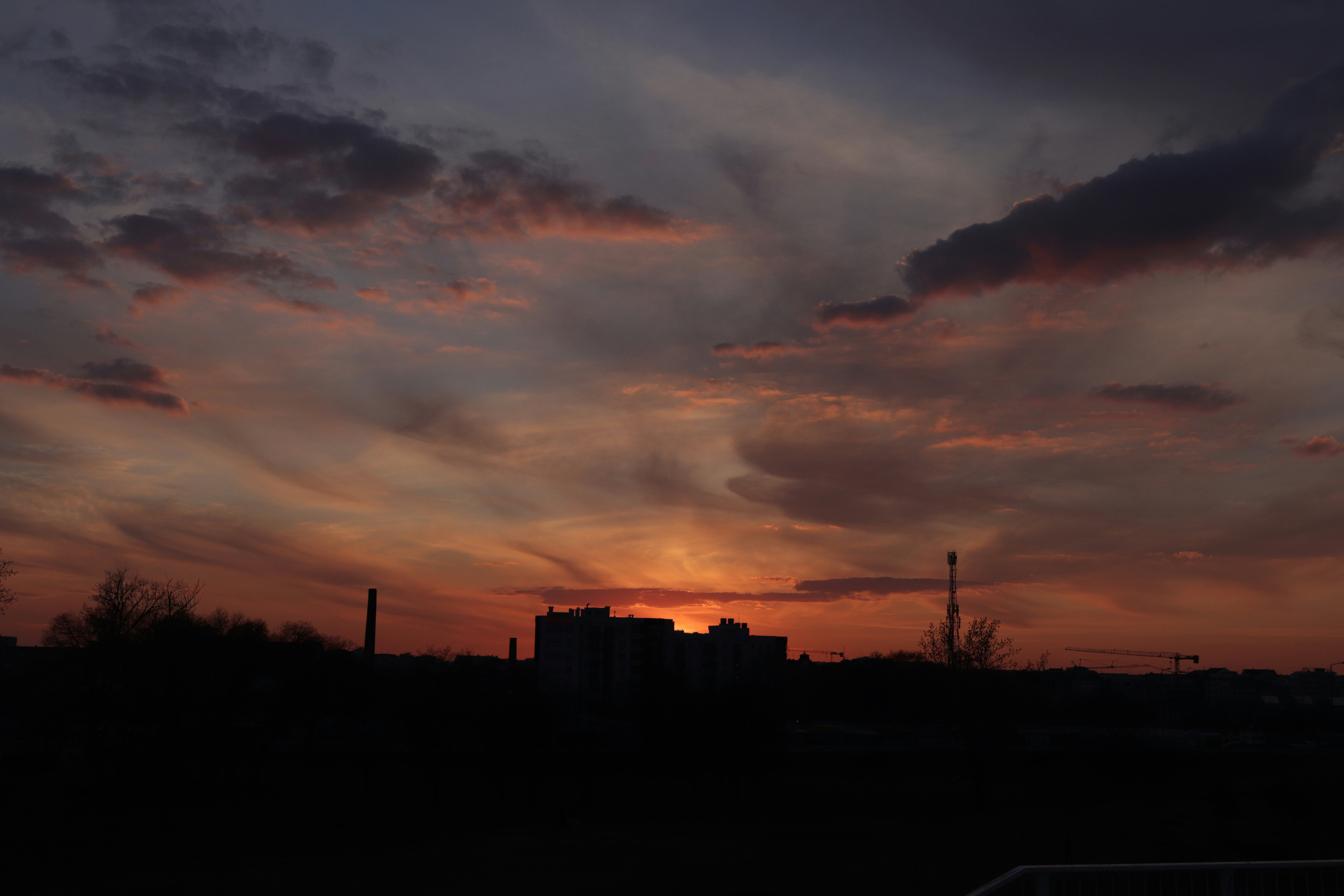 Silhouette of buildings against a vibrant sunset sky with scattered clouds.