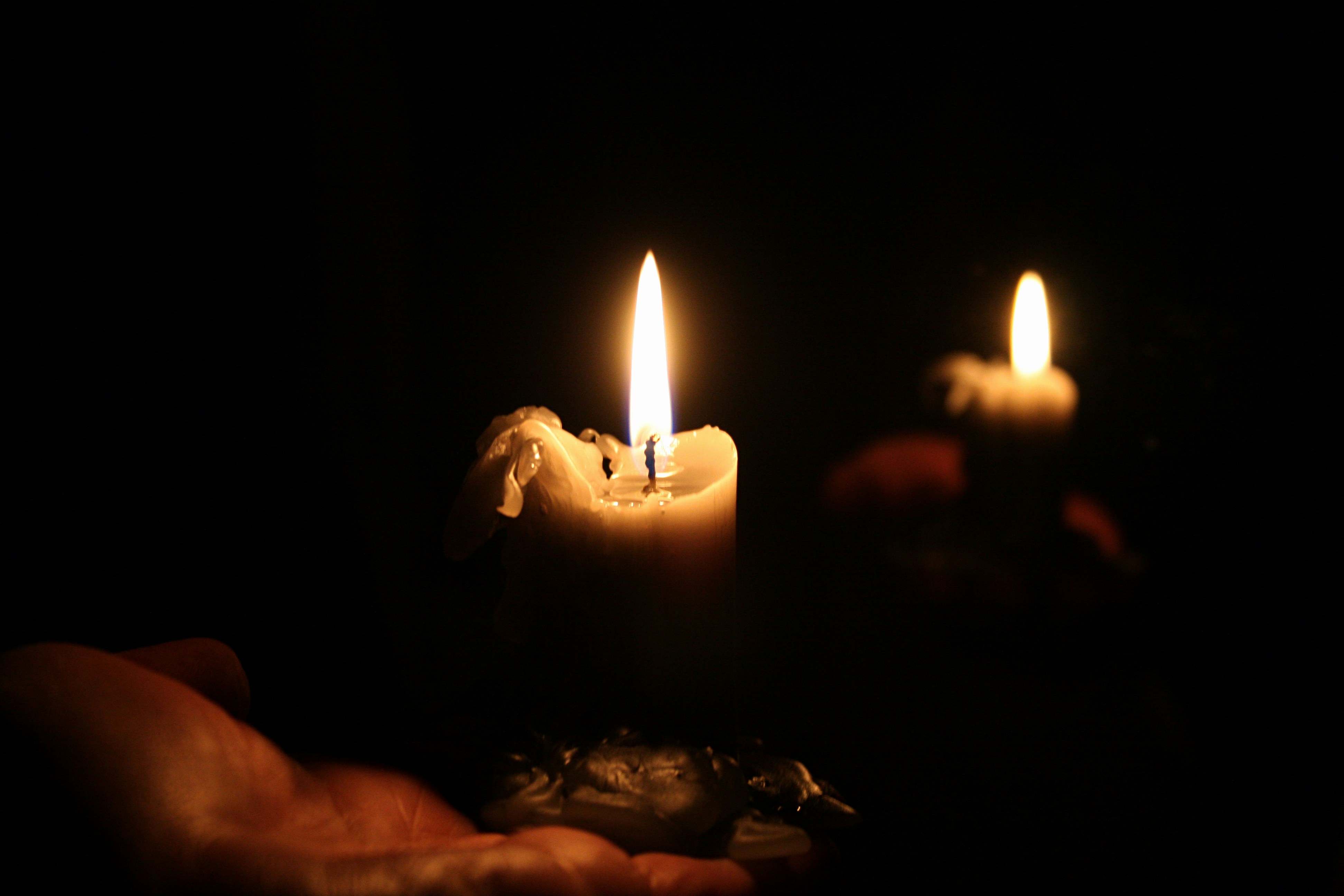 A glowing candle held gently in a hand, illuminating the surrounding darkness while casting a soft reflection nearby.