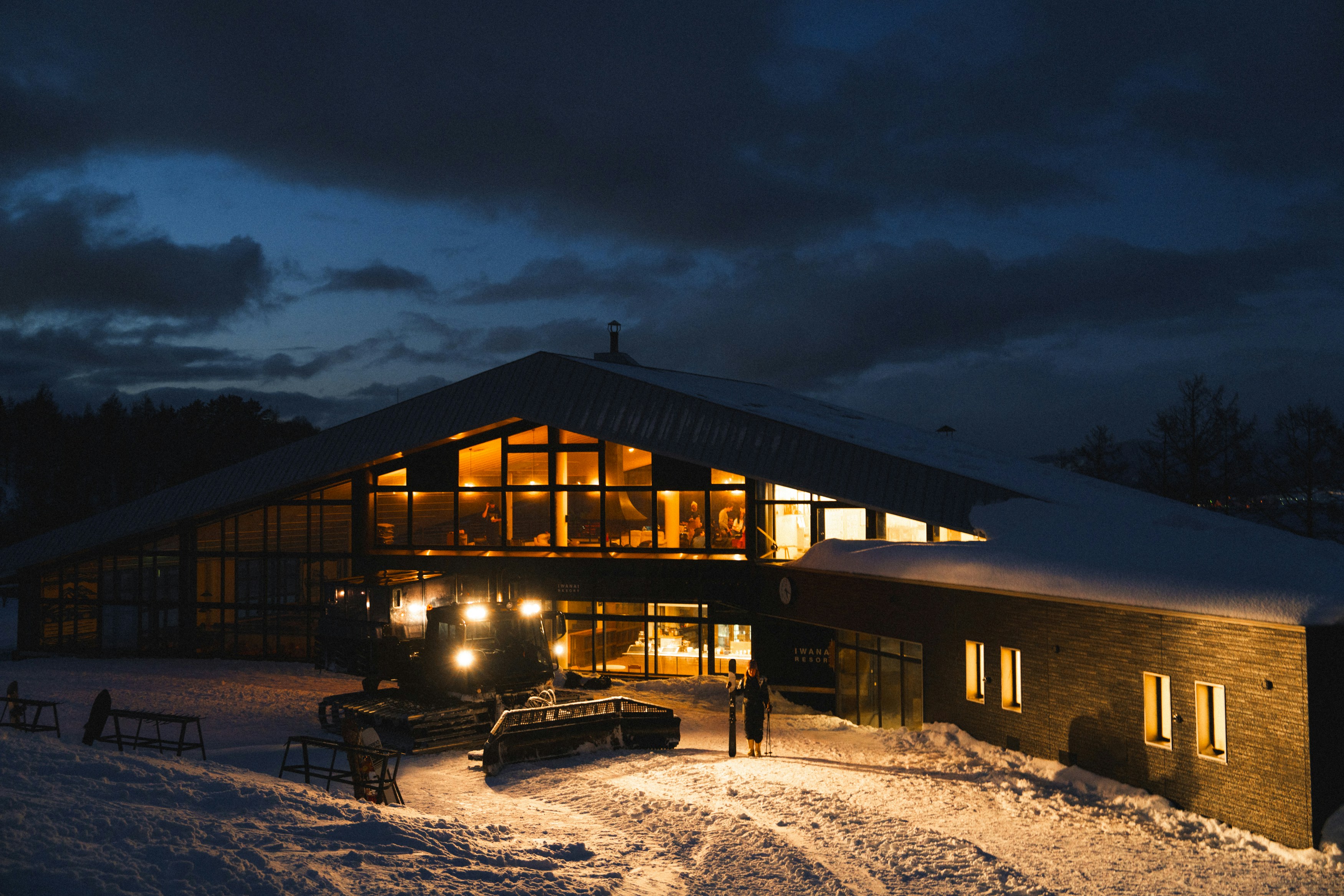 Warmly lit cabin nestled in a snow-covered landscape under a dusky sky.