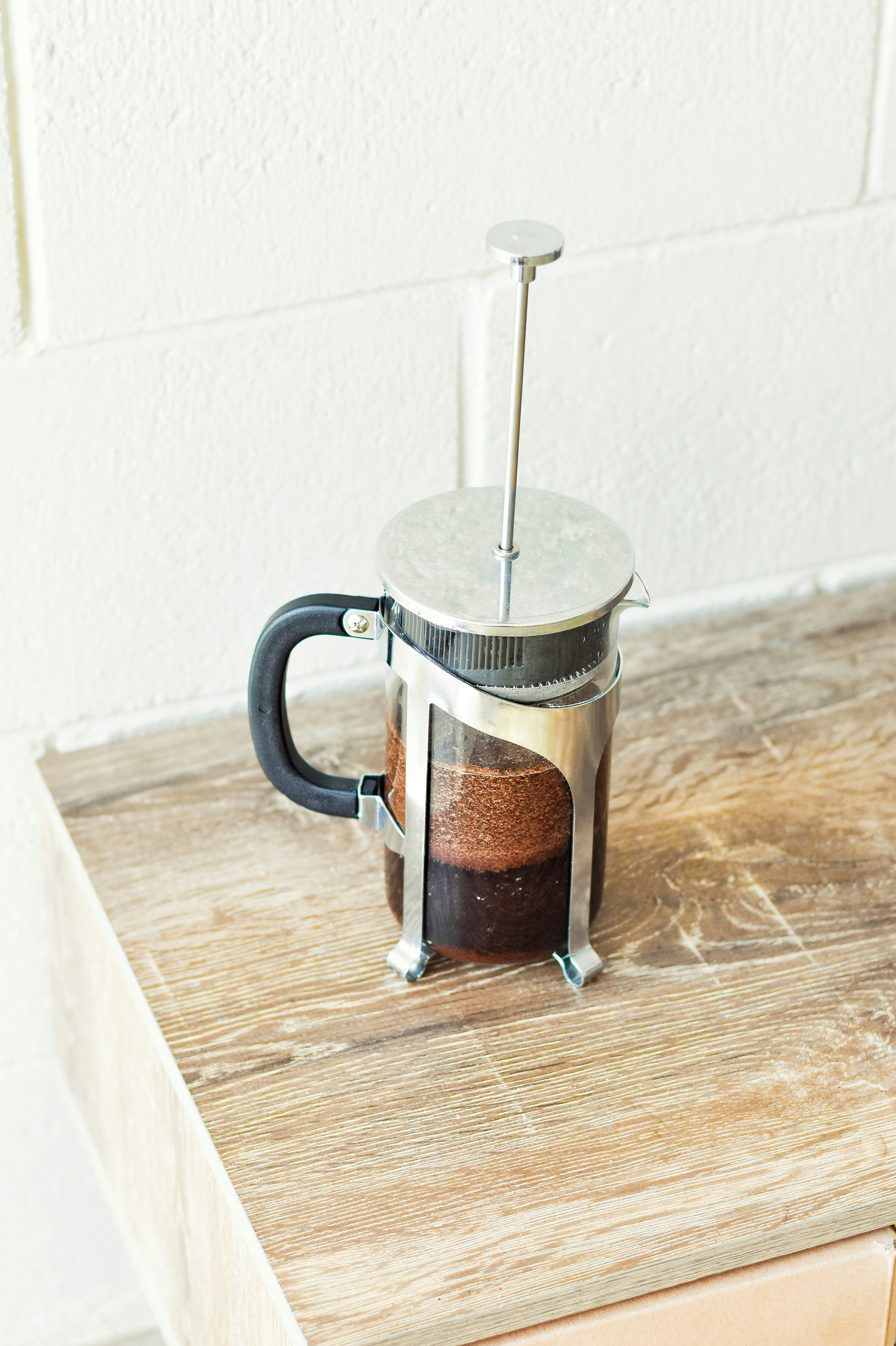 A French press sits elegantly on a wooden surface, showcasing the rich layers of coffee grounds and brewed coffee. The minimalist backdrop emphasizes the brewing process.