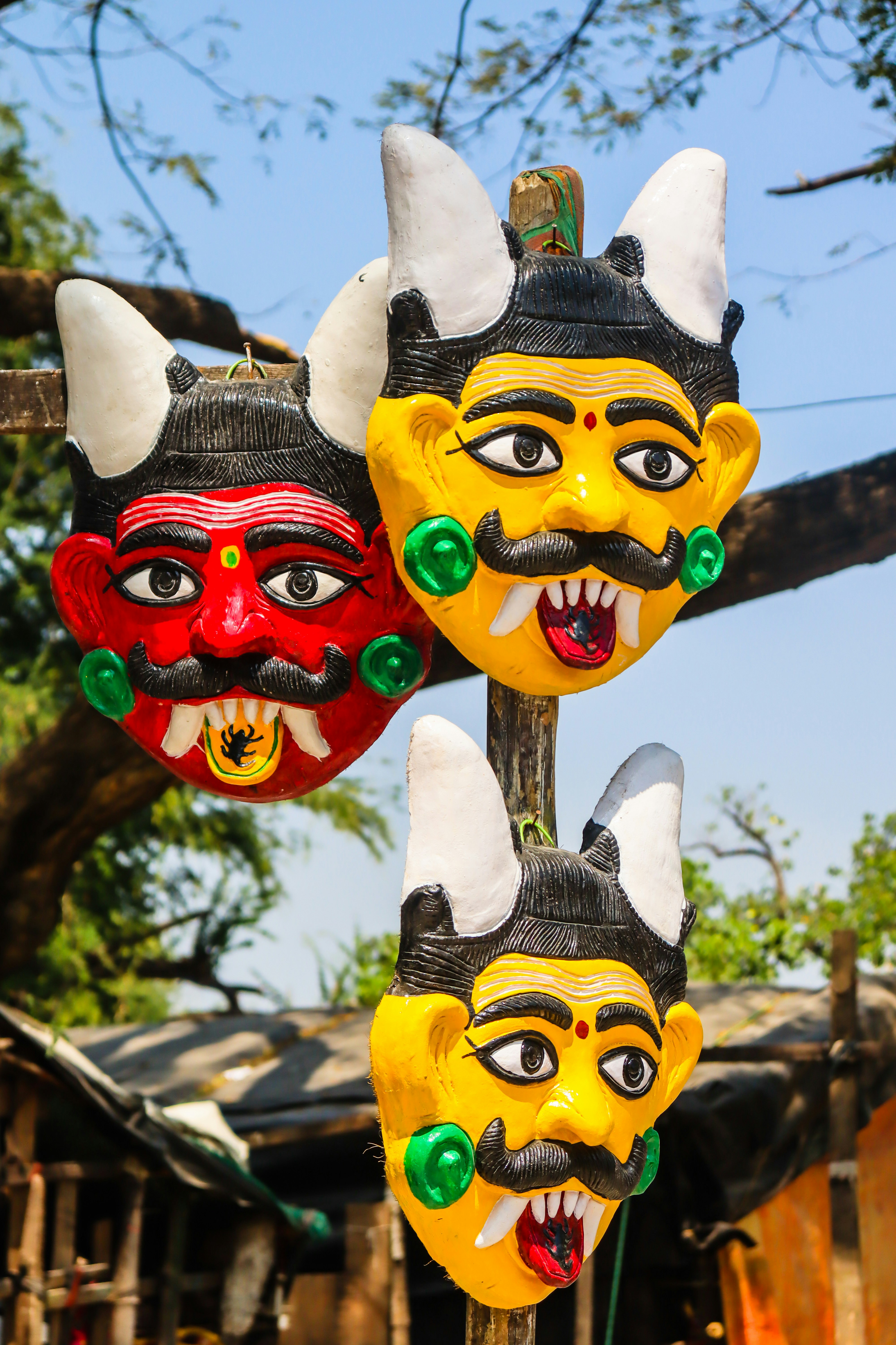 Sunlit Trio of Hand-Painted Demon Masks on a Rustic Post