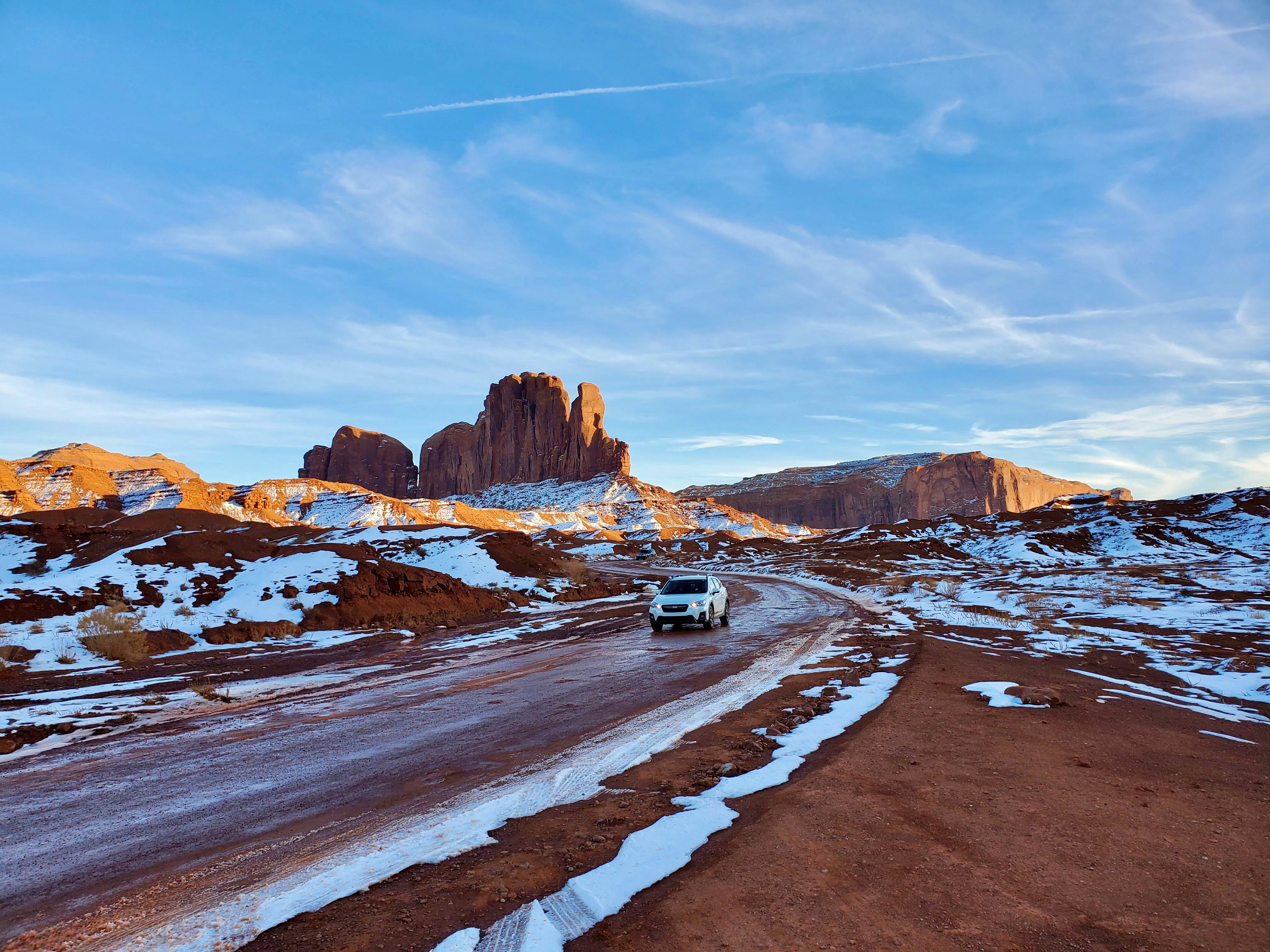 White Car on a Snow-Slashed Desert Road Toward Guardian Granite Monoliths