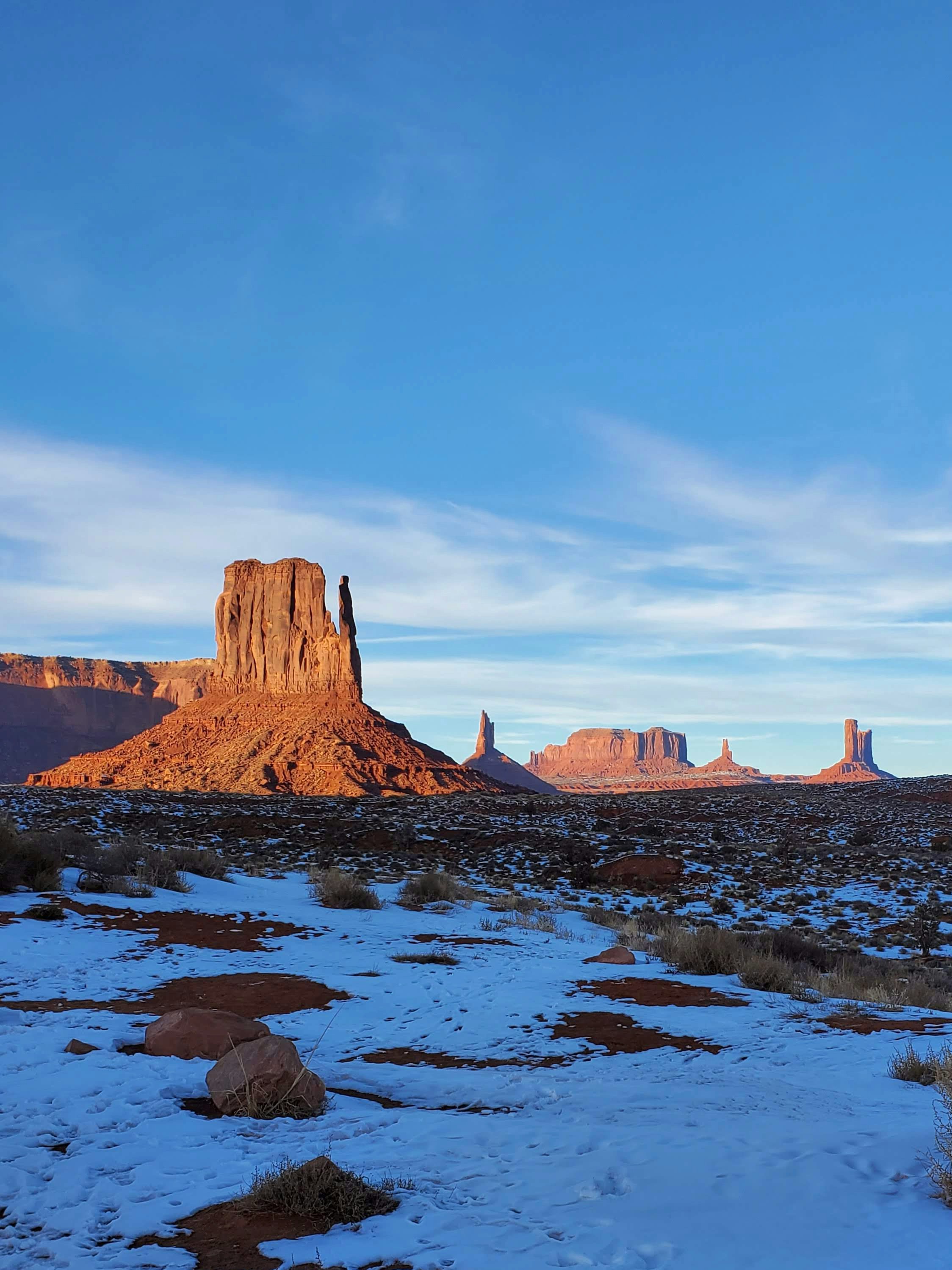 Snow-dusted desert landscape with towering sandstone buttes under a clear blue sky at Monument Valley.