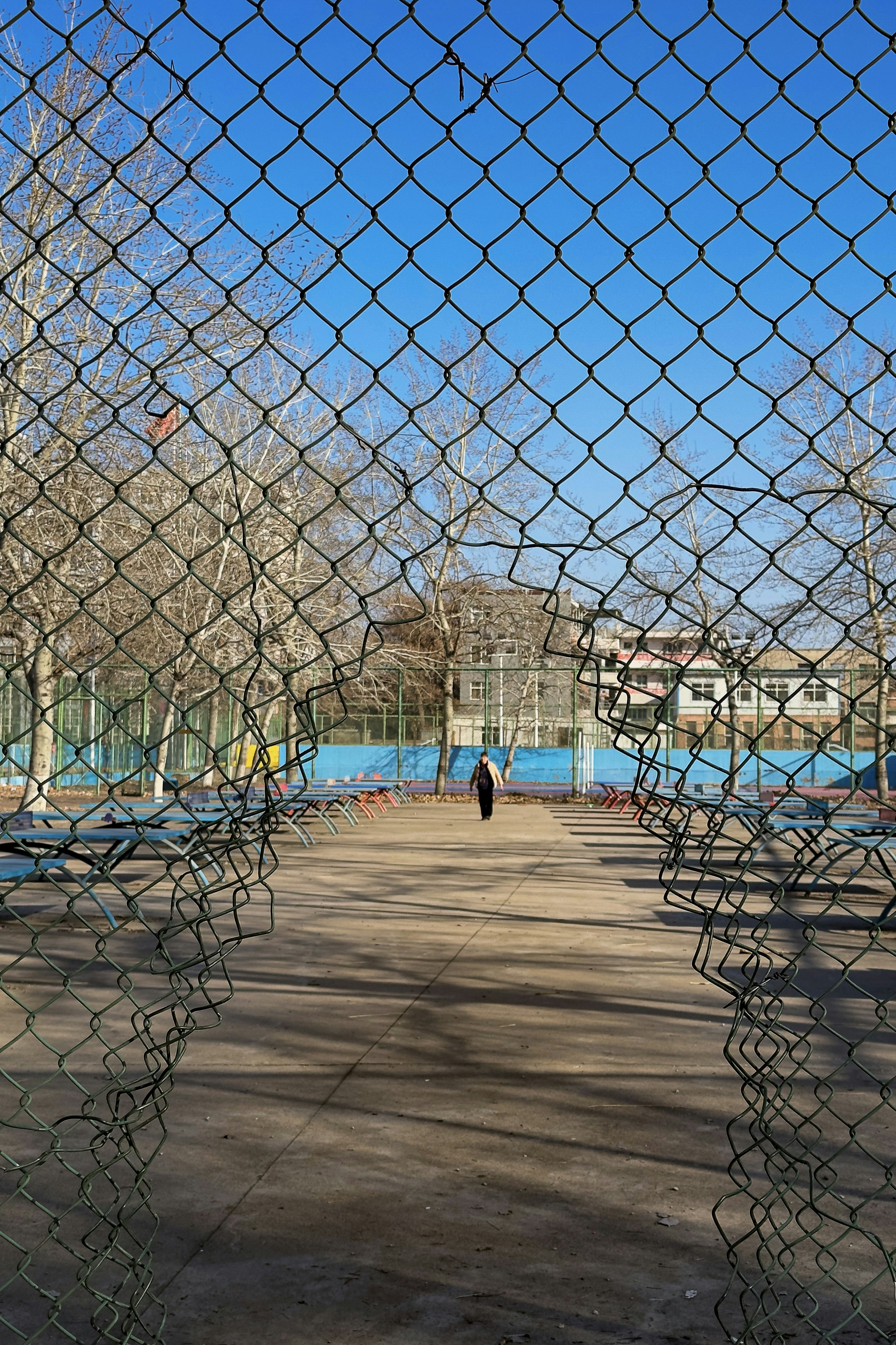 Center Court Through Diamond Mesh: A Lone Figure on a Sunlit Playground