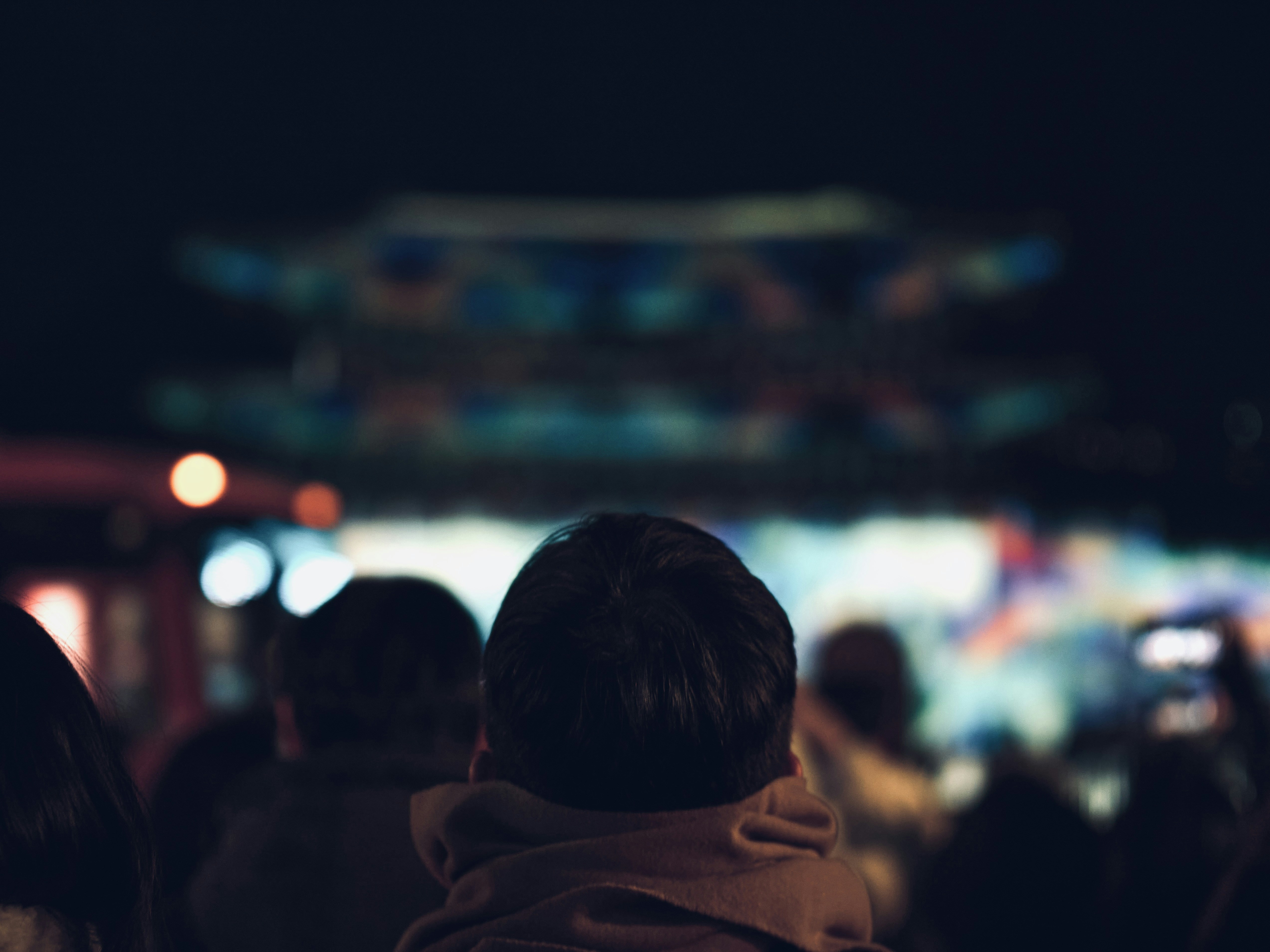 Back of a person's head in a crowd with colorful lights in the background at night.