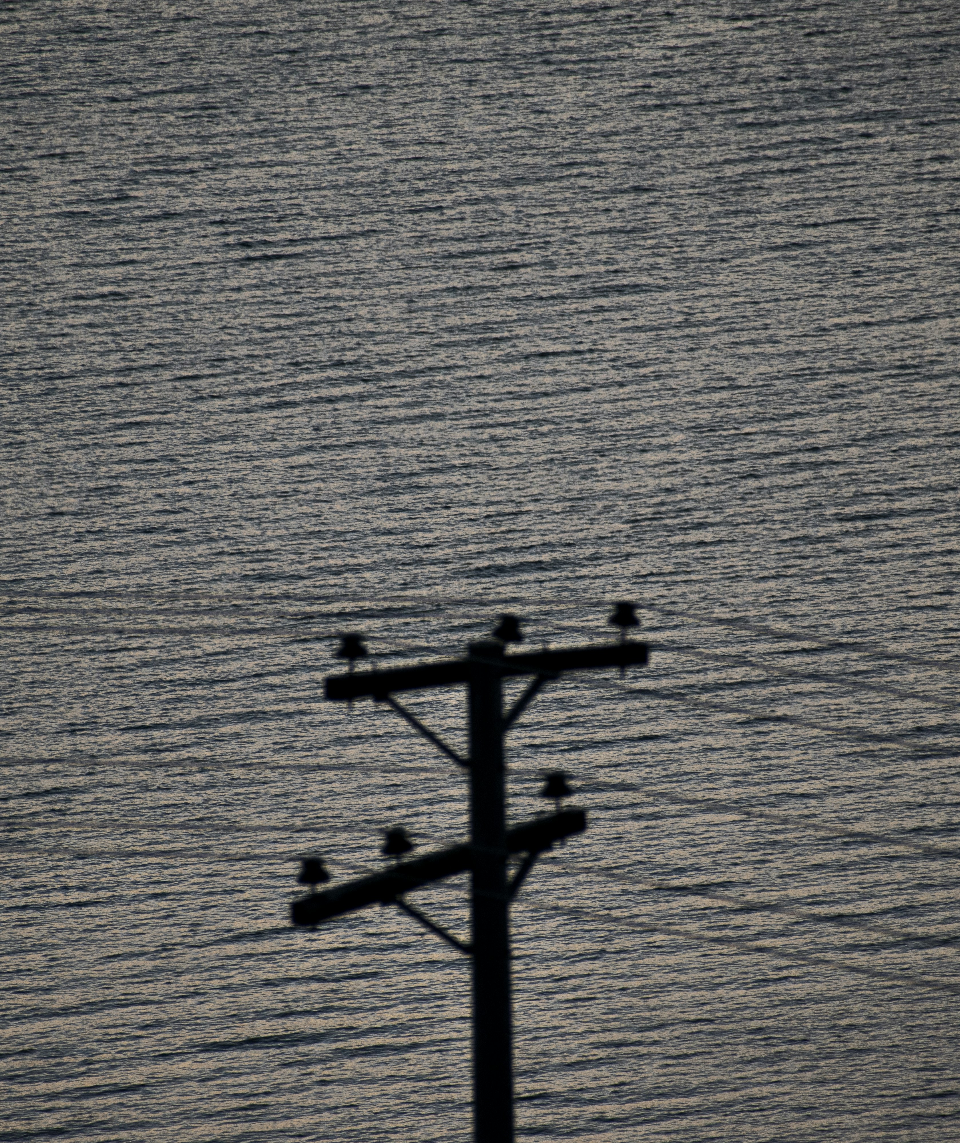 Lone Power Pole at Dusk: Silhouette Over Rippled Water