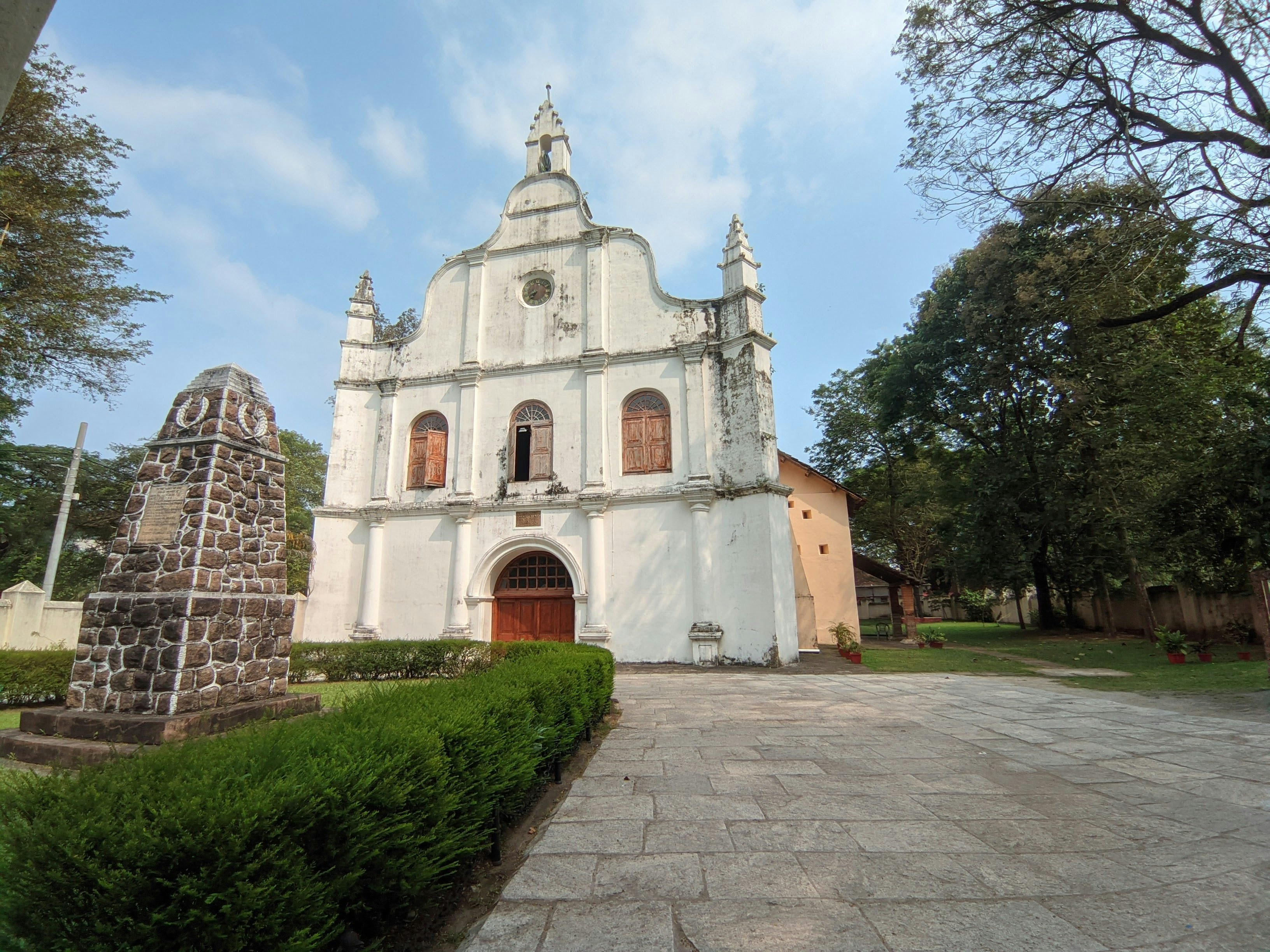 White colonial-style church with arched entrance and symmetrical towers, surrounded by lush greenery.