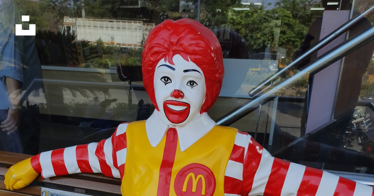 A Statue Of A Ronald Mcdonald Sitting On A Bench Photo Free Coat