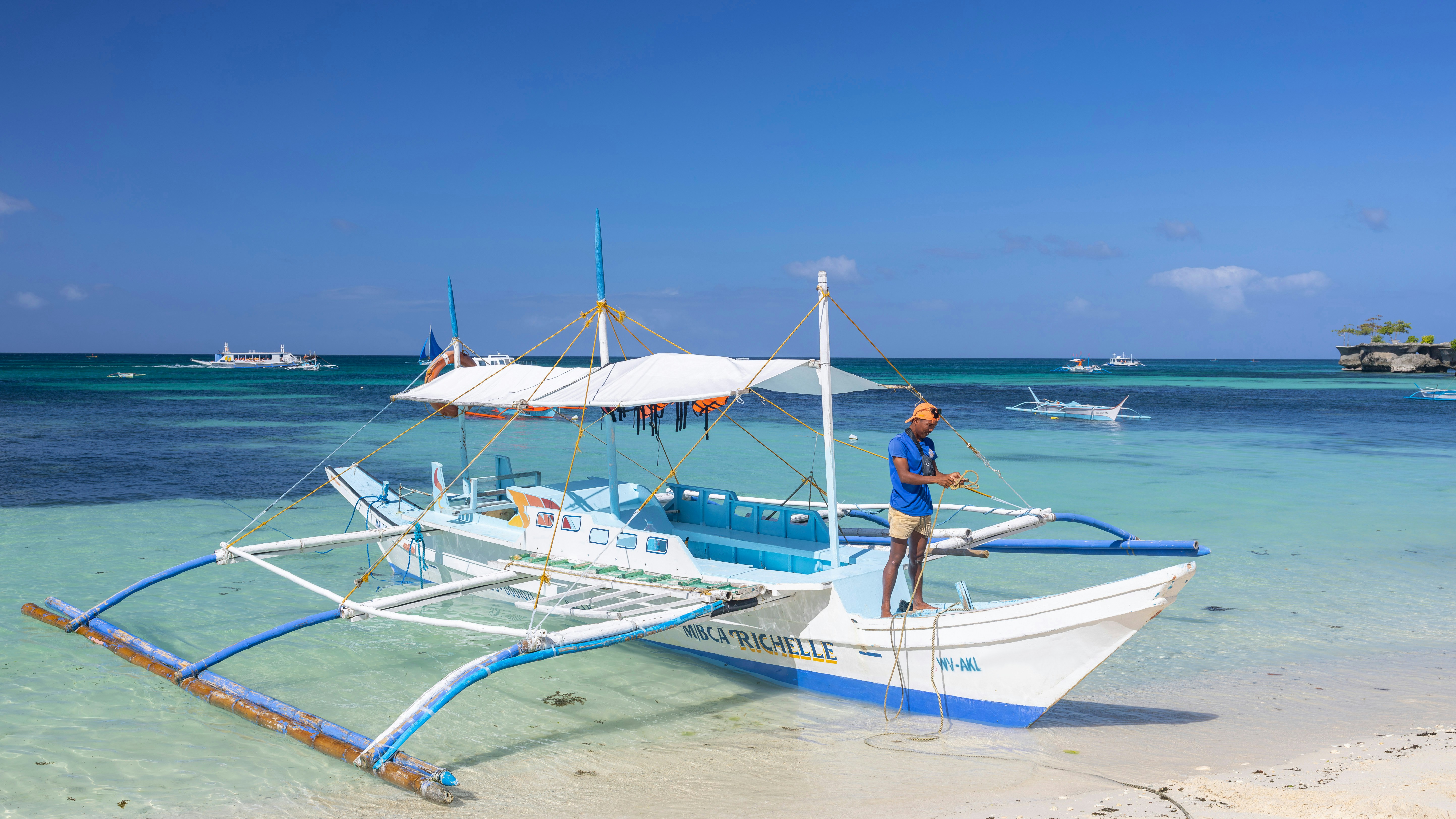 Traditional Filipino bangka anchored in clear turquoise waters, with a fisherman preparing for the day’s catch.