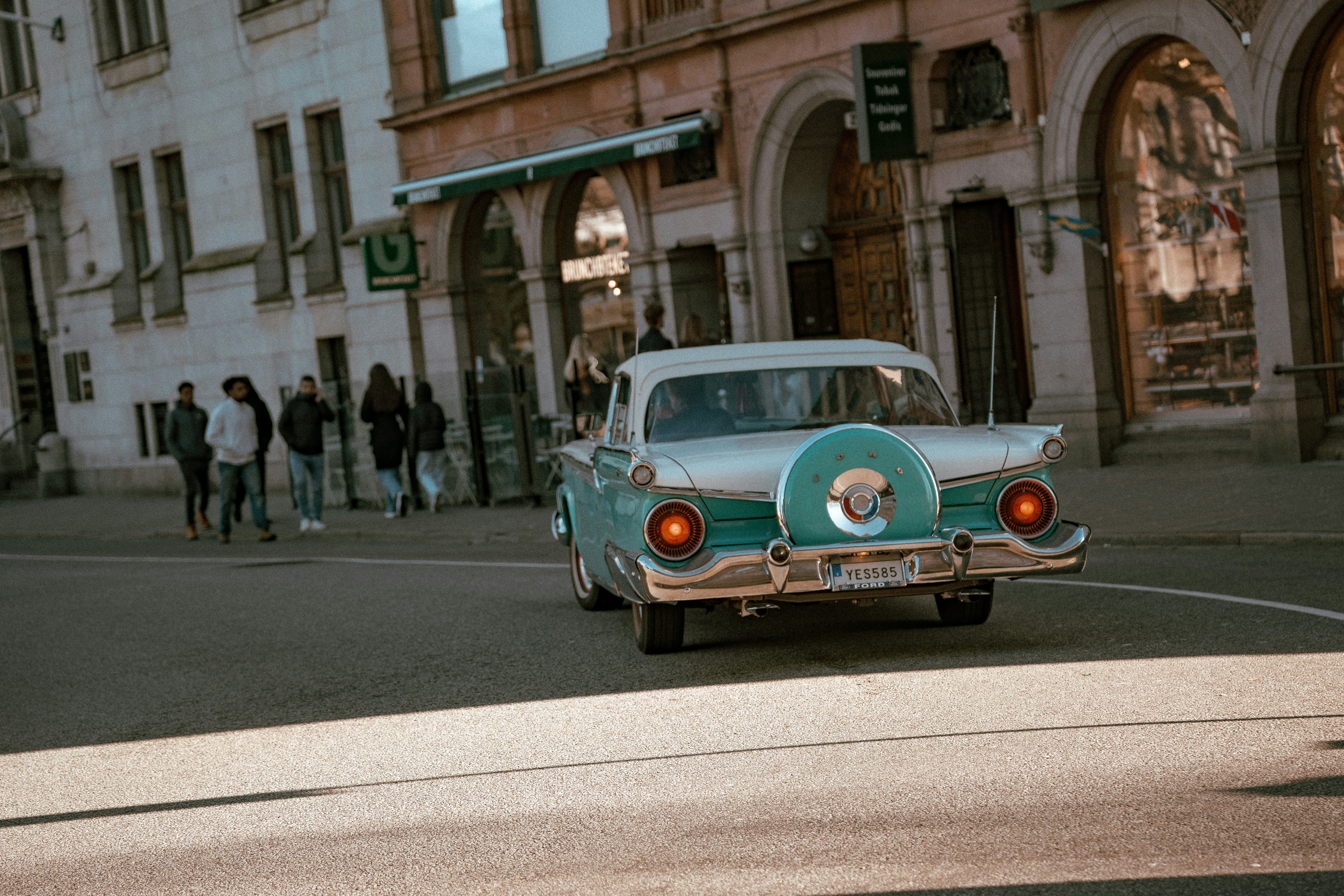 Classic car making a turn on a city street, showcasing its vintage design against a backdrop of modern architecture.