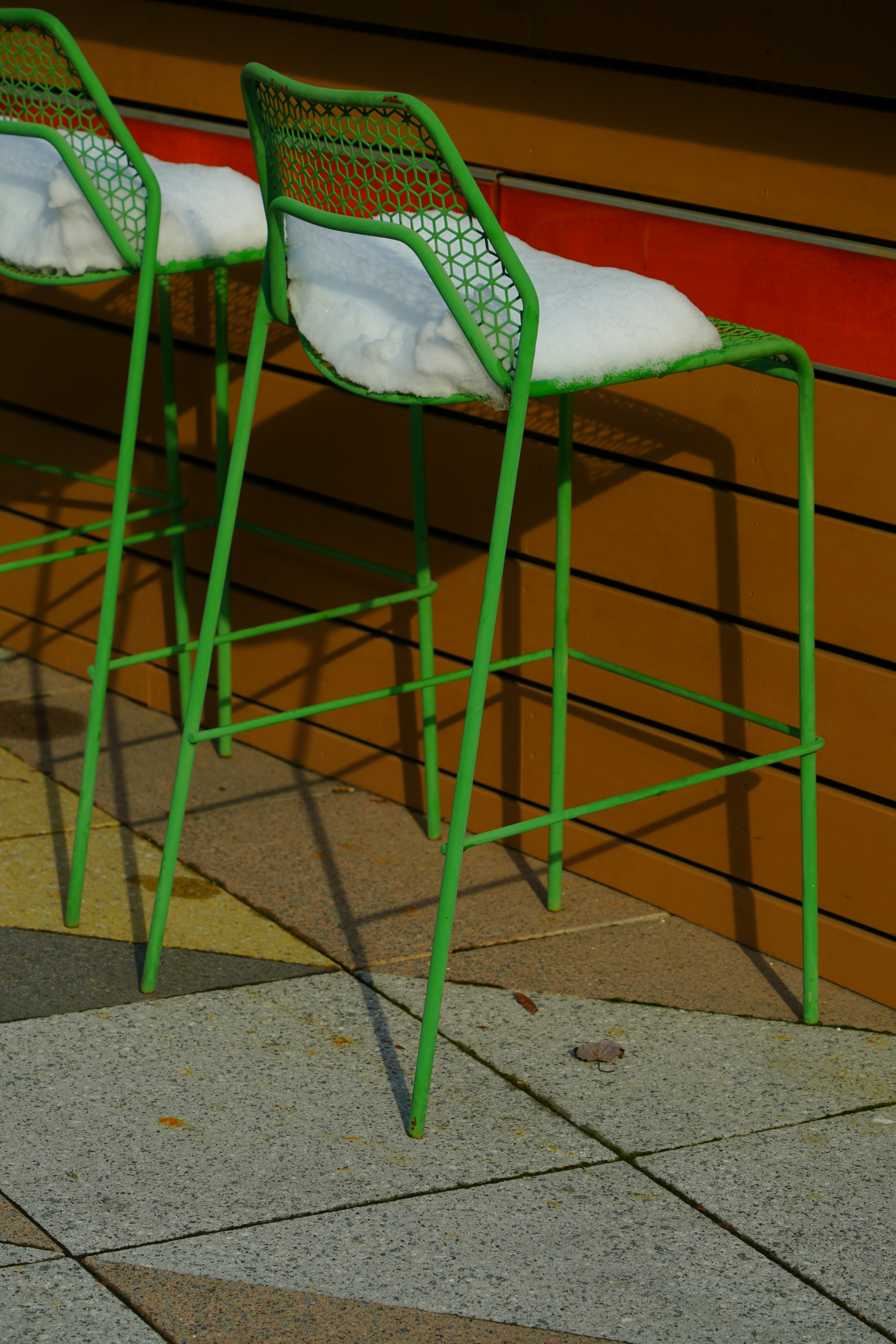 Snow-dusted Green Metal Stools Along a Sunlit Wooden Wall