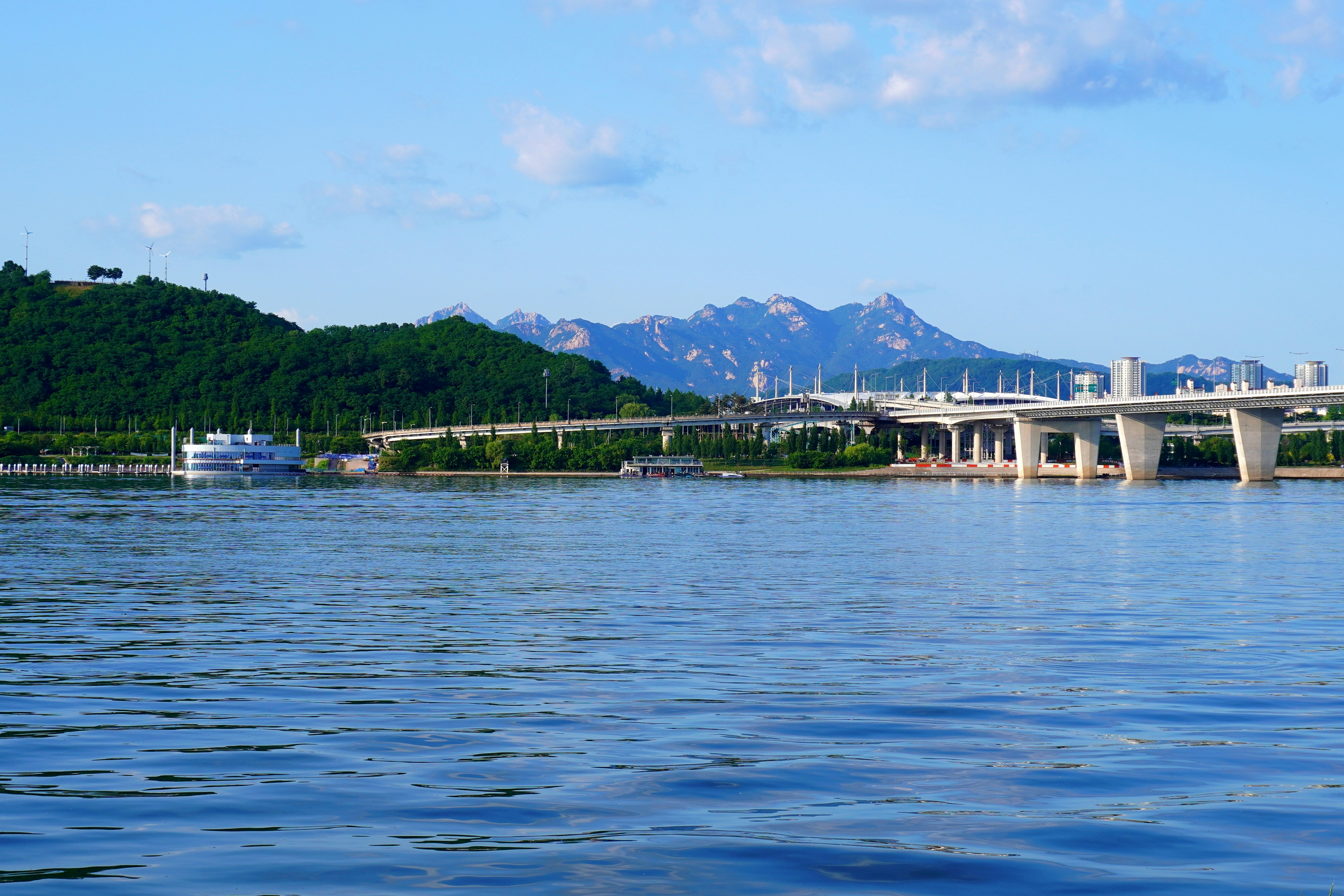 Bridge Ribbon Over a Quiet Bay, Framing Green Hills and Snow-Dusted Peaks