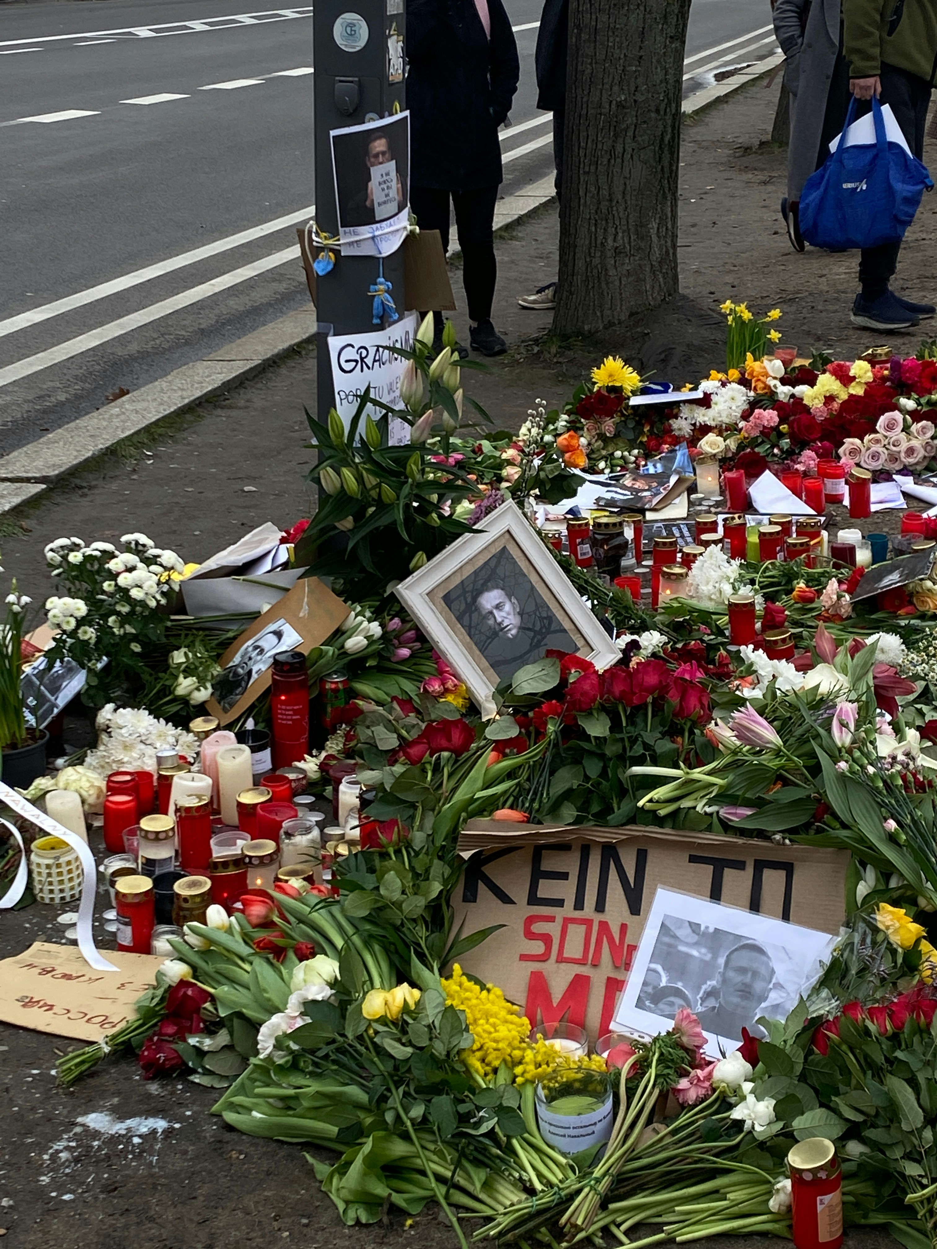 Bouquets, candles, and portraits at a roadside memorial
