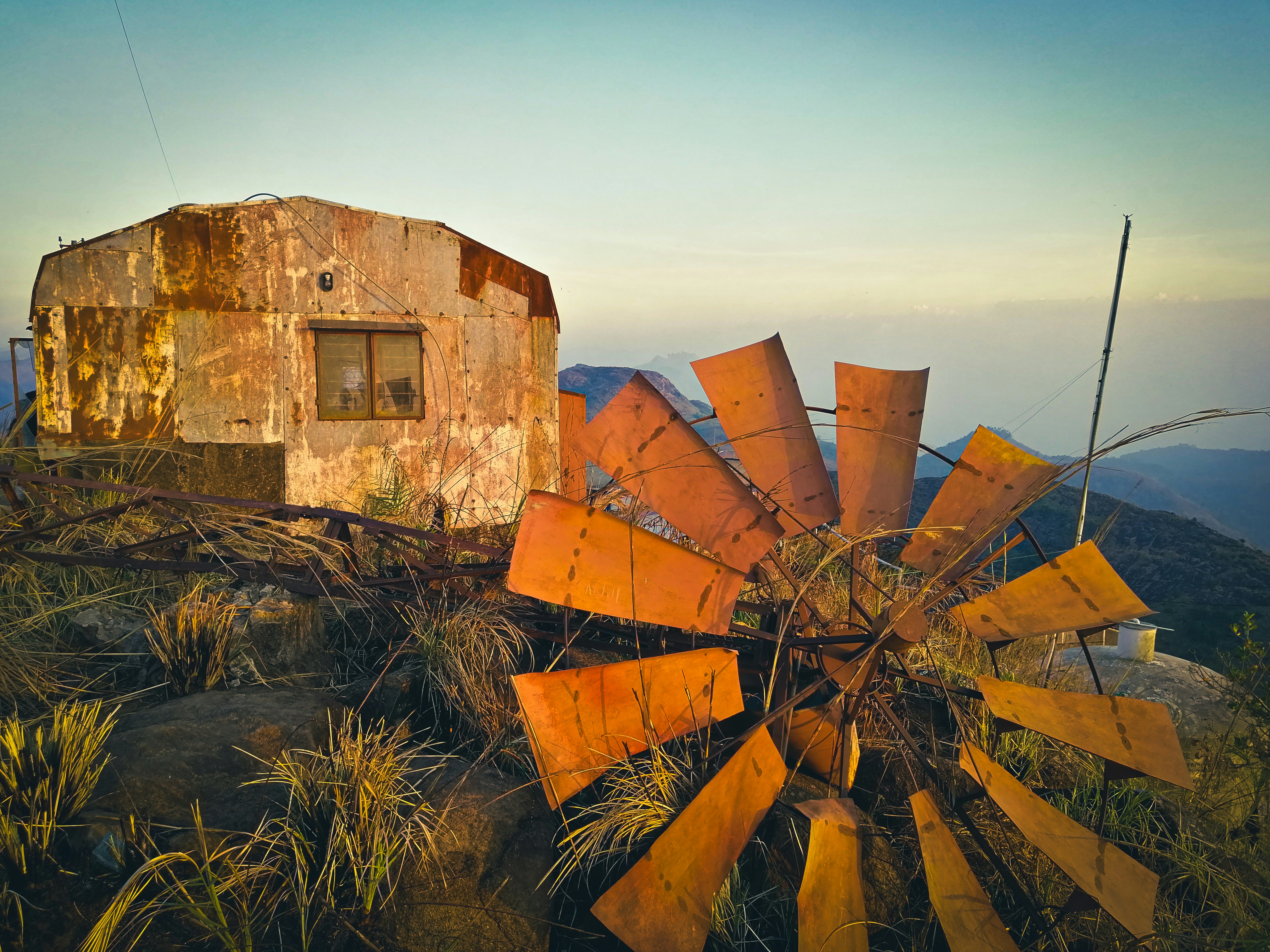 A rusted windmill sitting on top of a lush green hillside photo – Free ...
