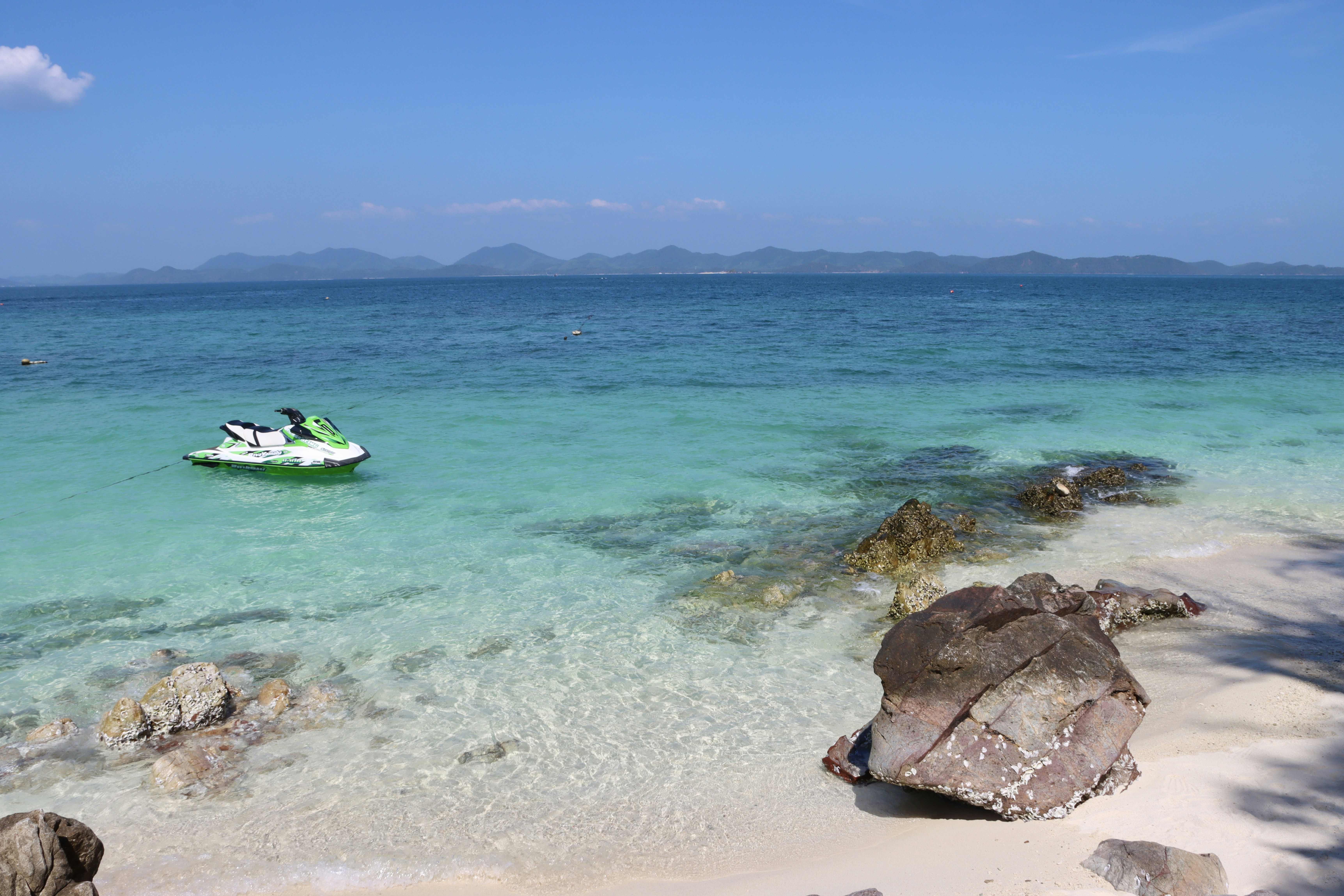 Jet ski gliding on clear turquoise waters near a rocky shoreline under a bright blue sky.