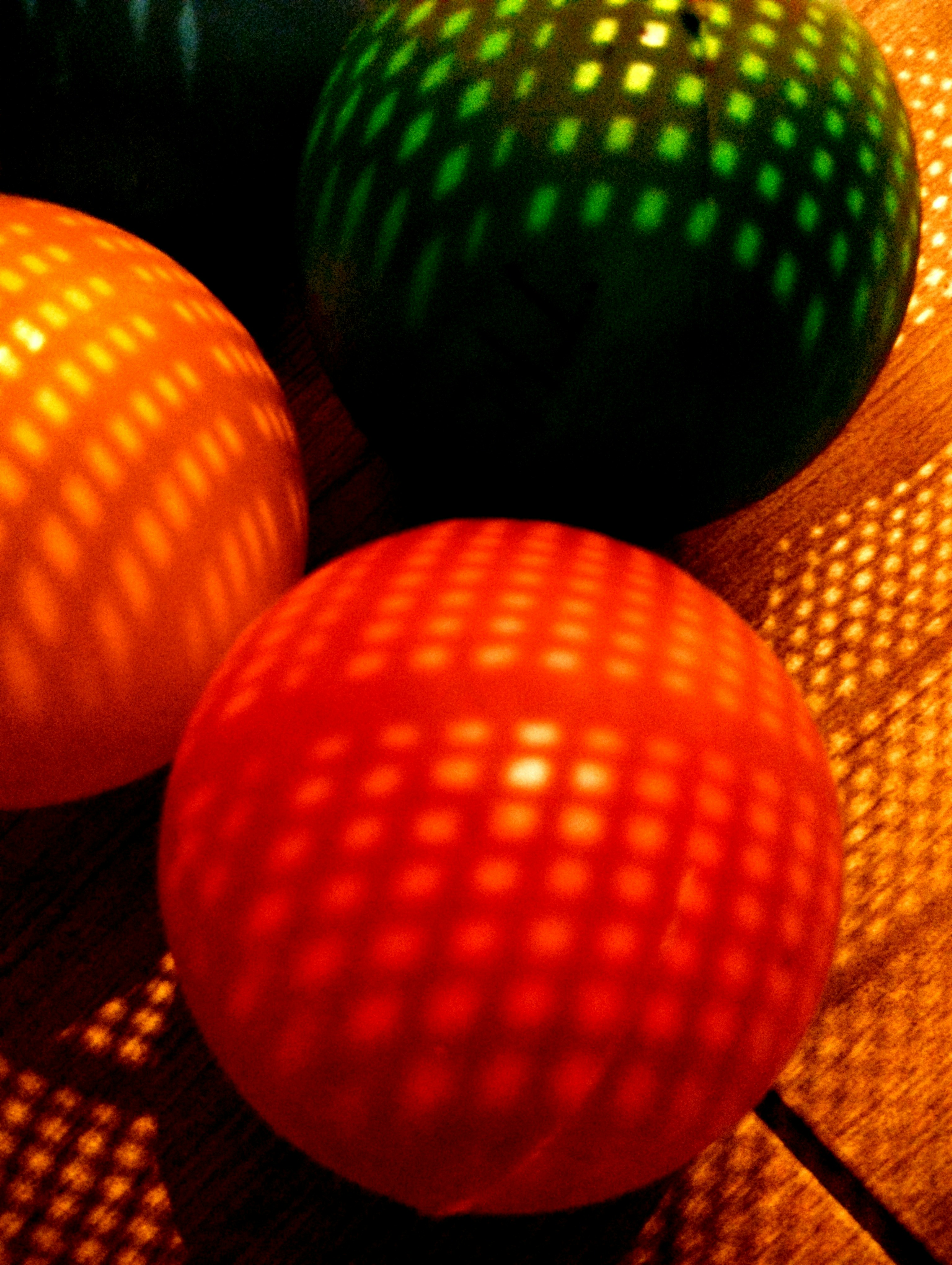 Orange, red, and green spheres sit on a wooden surface, with a grid of dotted light patterns projecting across them.