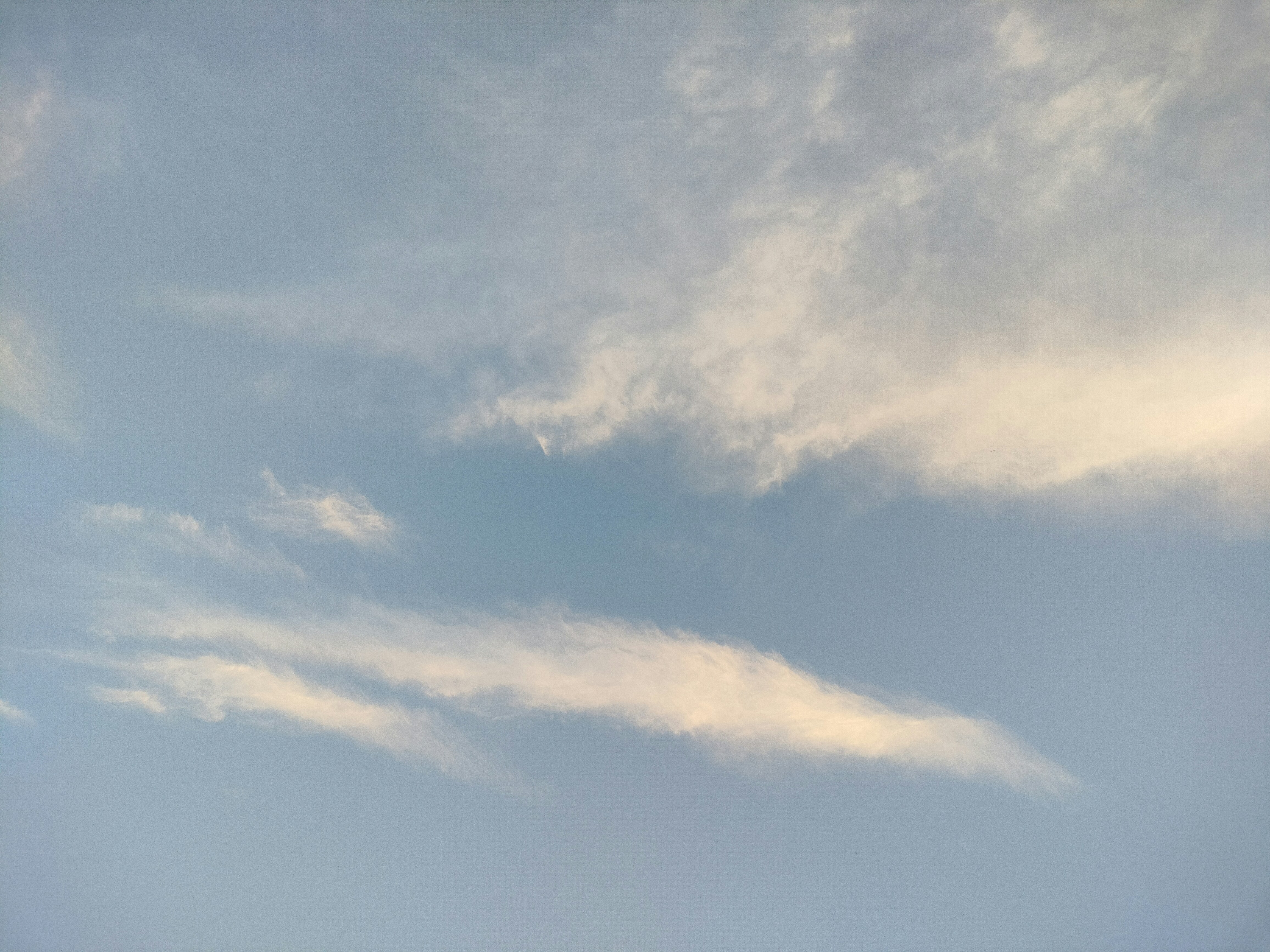 Soft clouds drift across a serene blue sky as daylight fades.