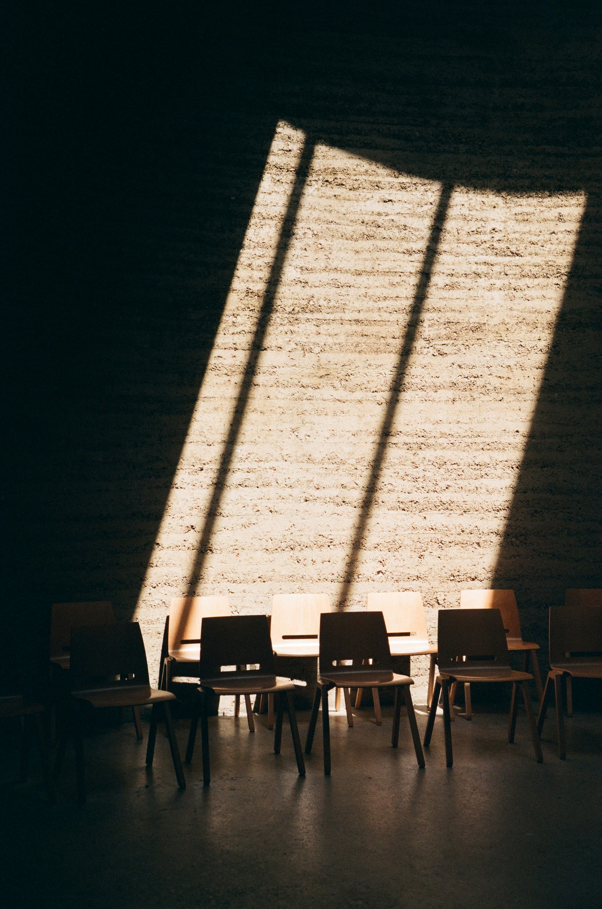 Wooden chairs aligned against a wall, illuminated by dramatic diagonal sunlight.