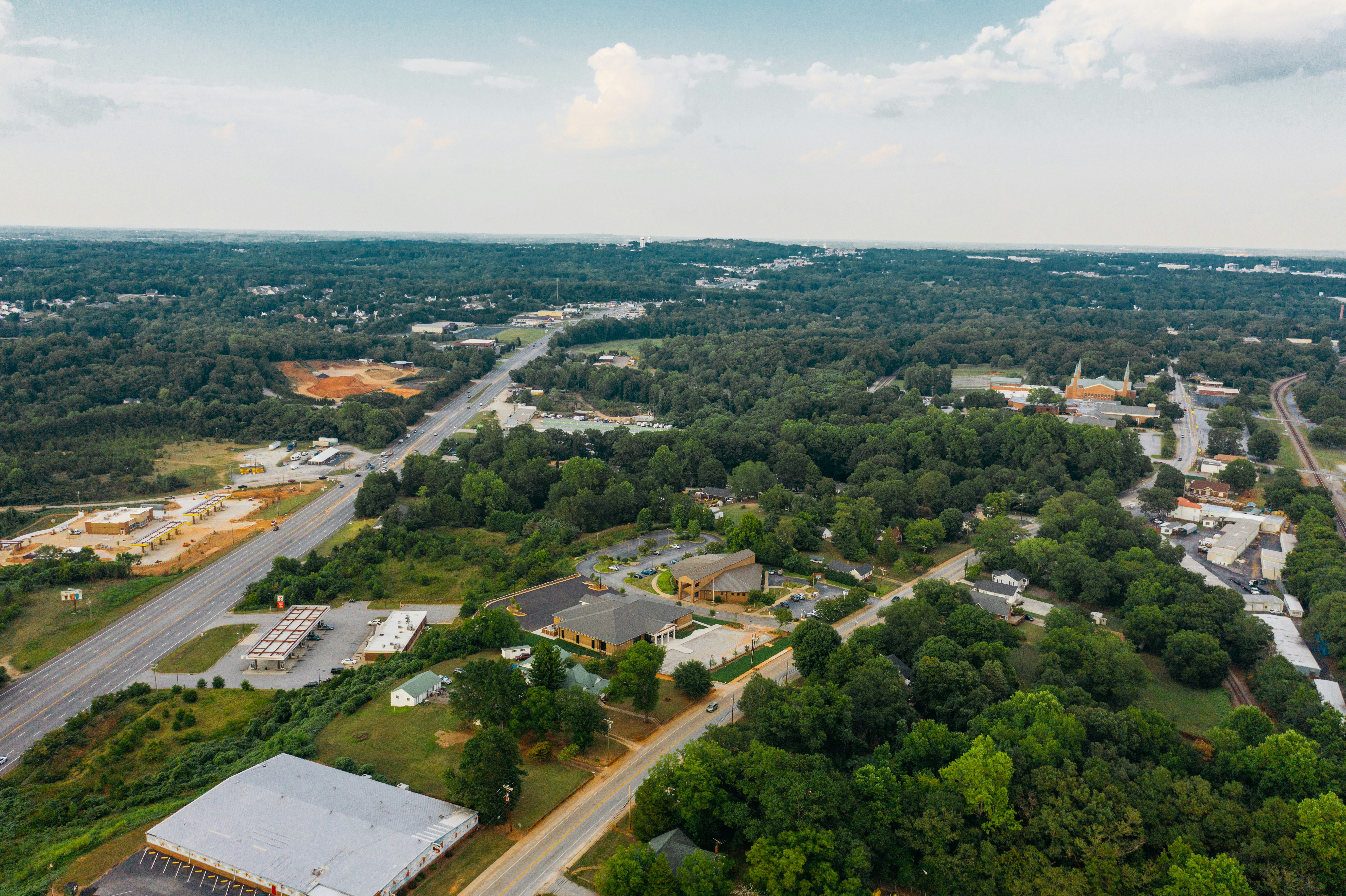 Expansive aerial view of a suburban landscape with roads winding through lush greenery under a partly cloudy sky.