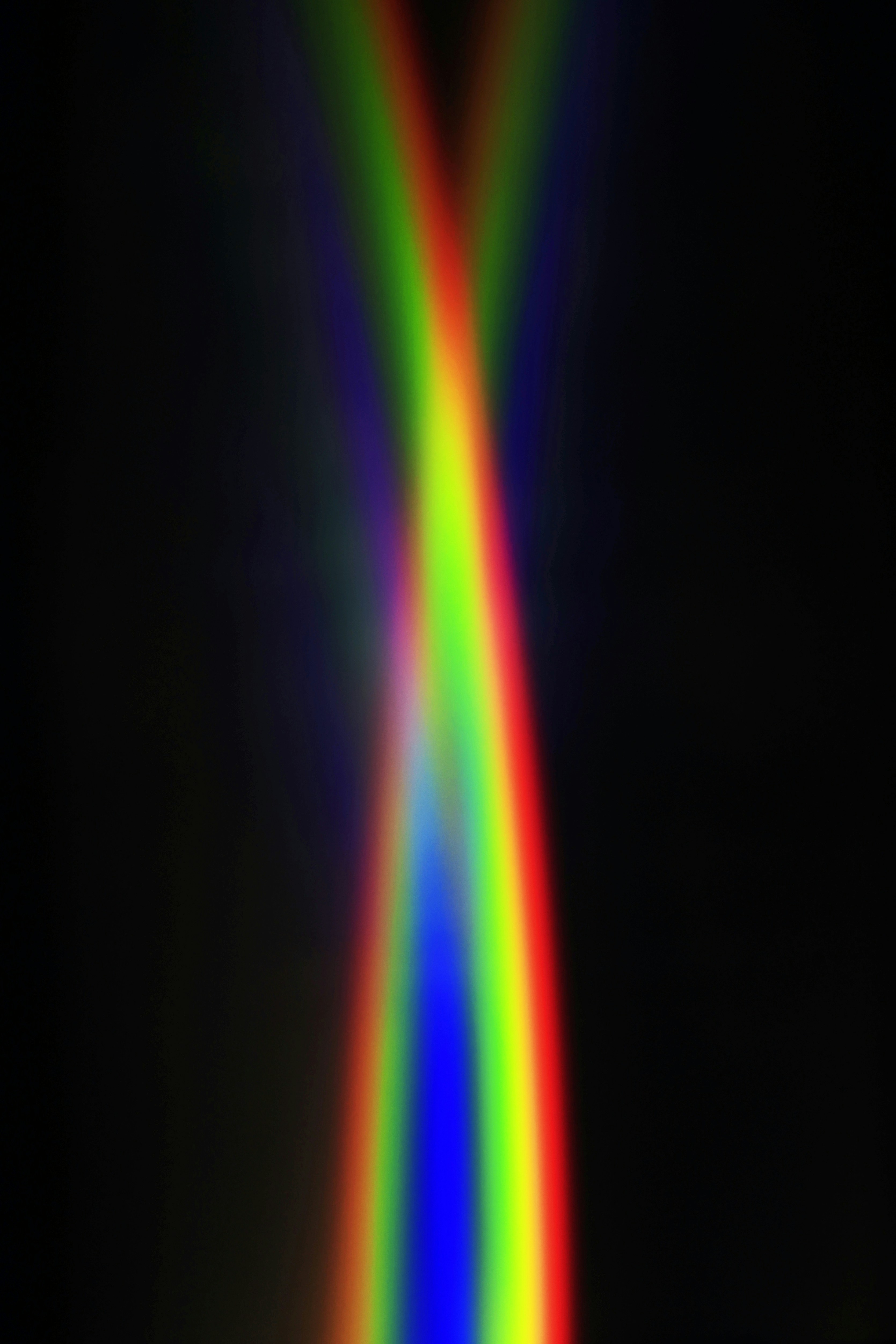 A rainbow colored object in the middle of a black background photo ...