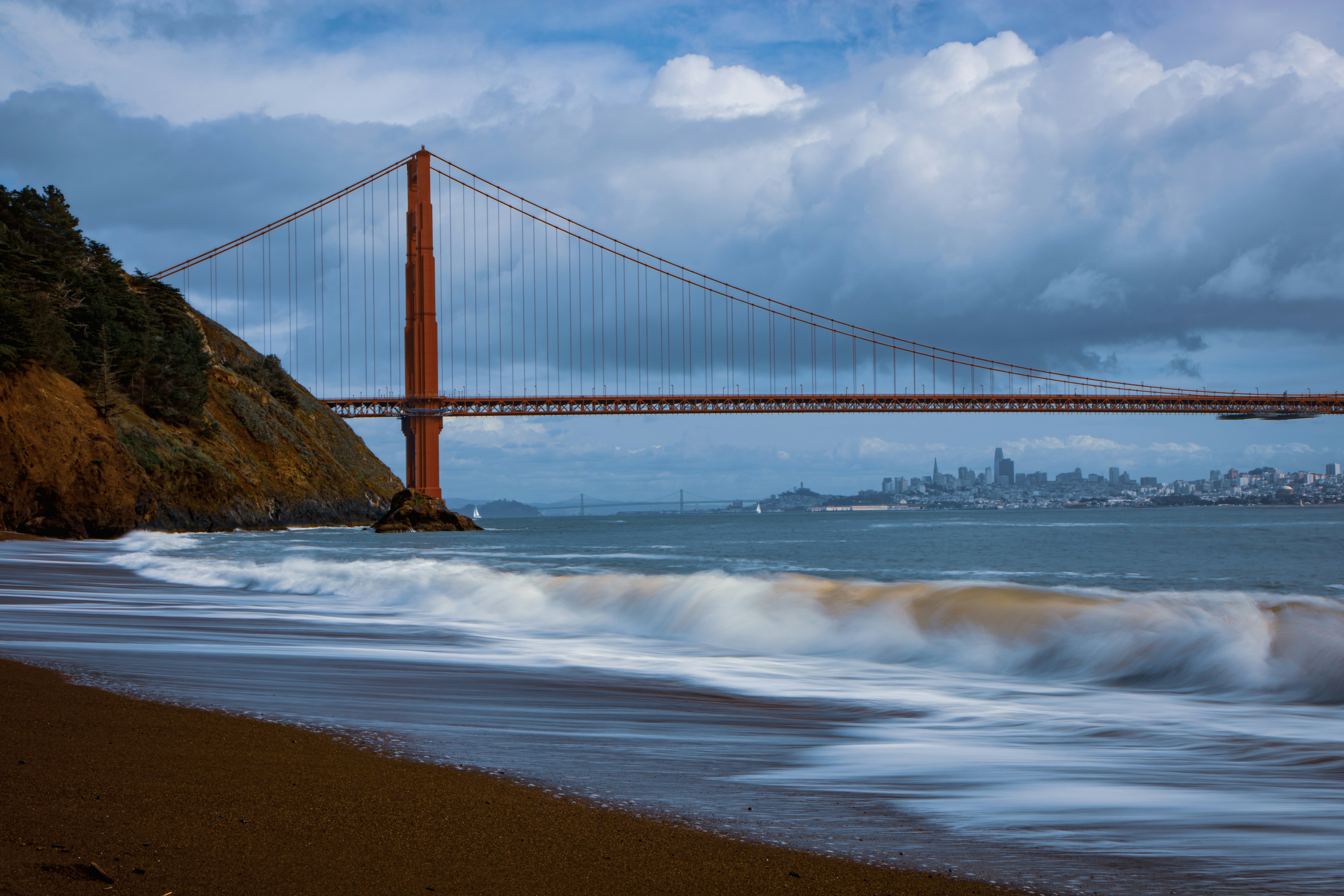 Red Span Over the Bay: Golden Gate Bridge Framed by Surf and Distant Skyline