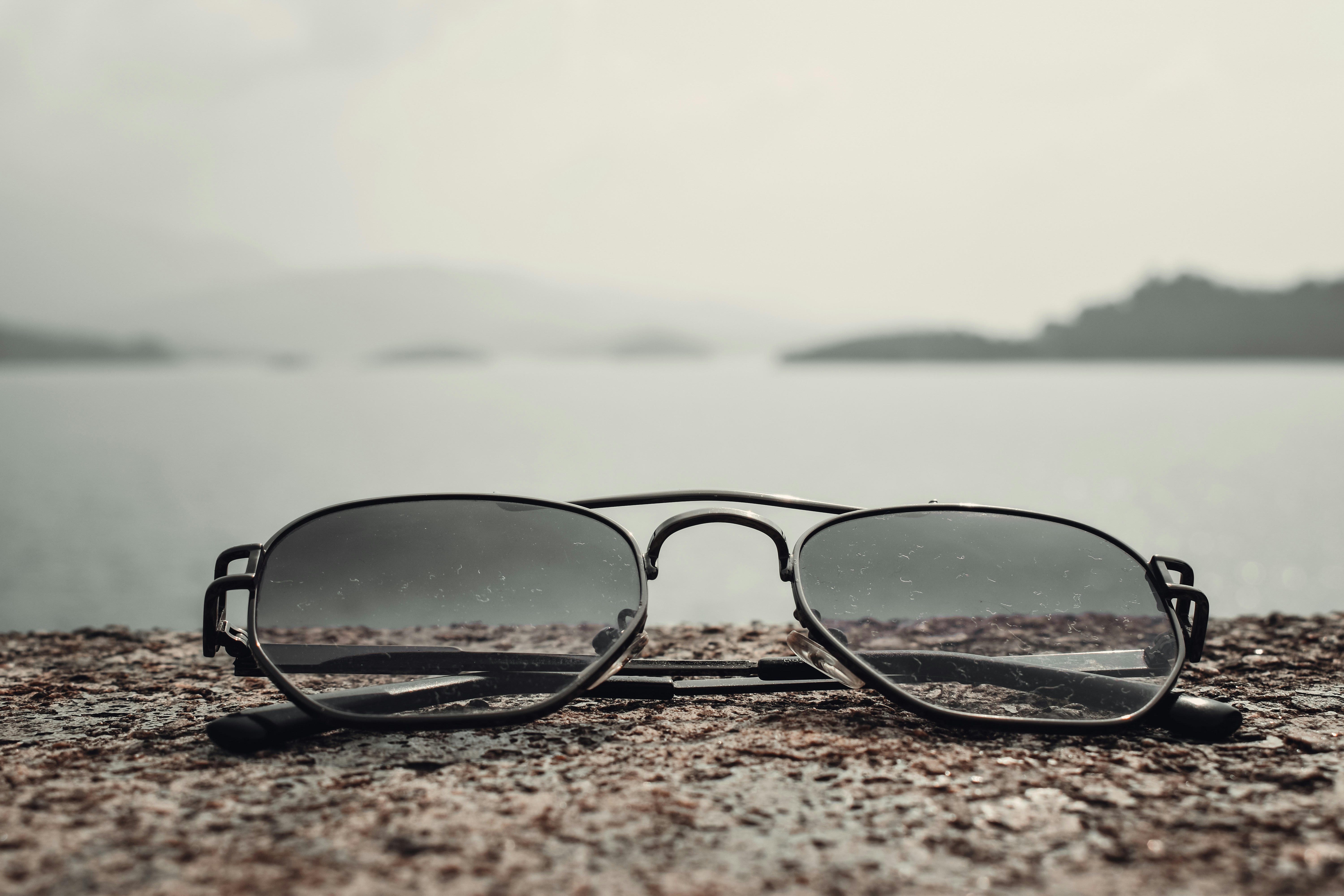 Centered Gaze: Sunglasses Rest on Weathered Stone by a Quiet Lake