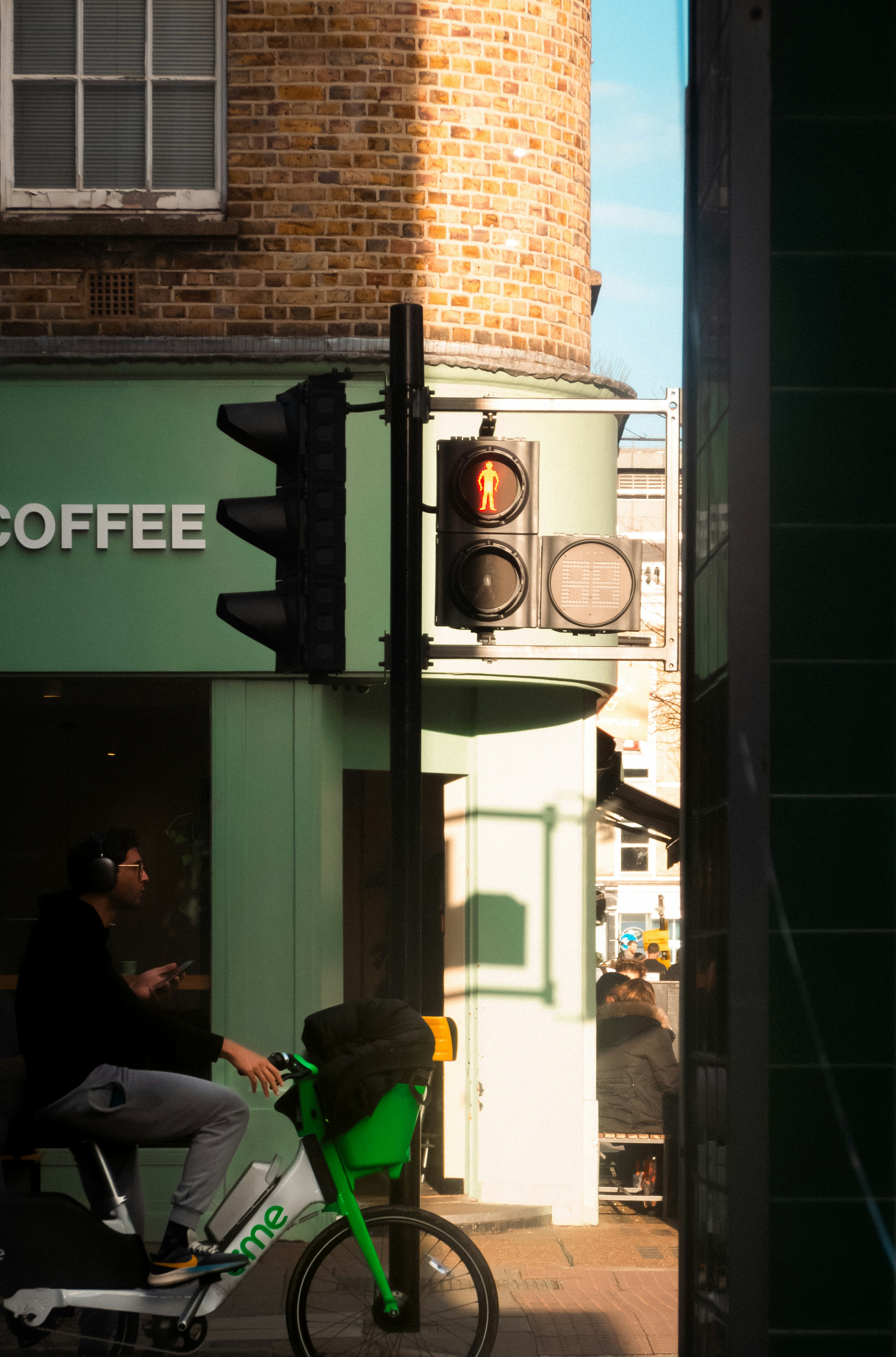 Cyclist waits at a red light near a coffee shop under warm afternoon light.