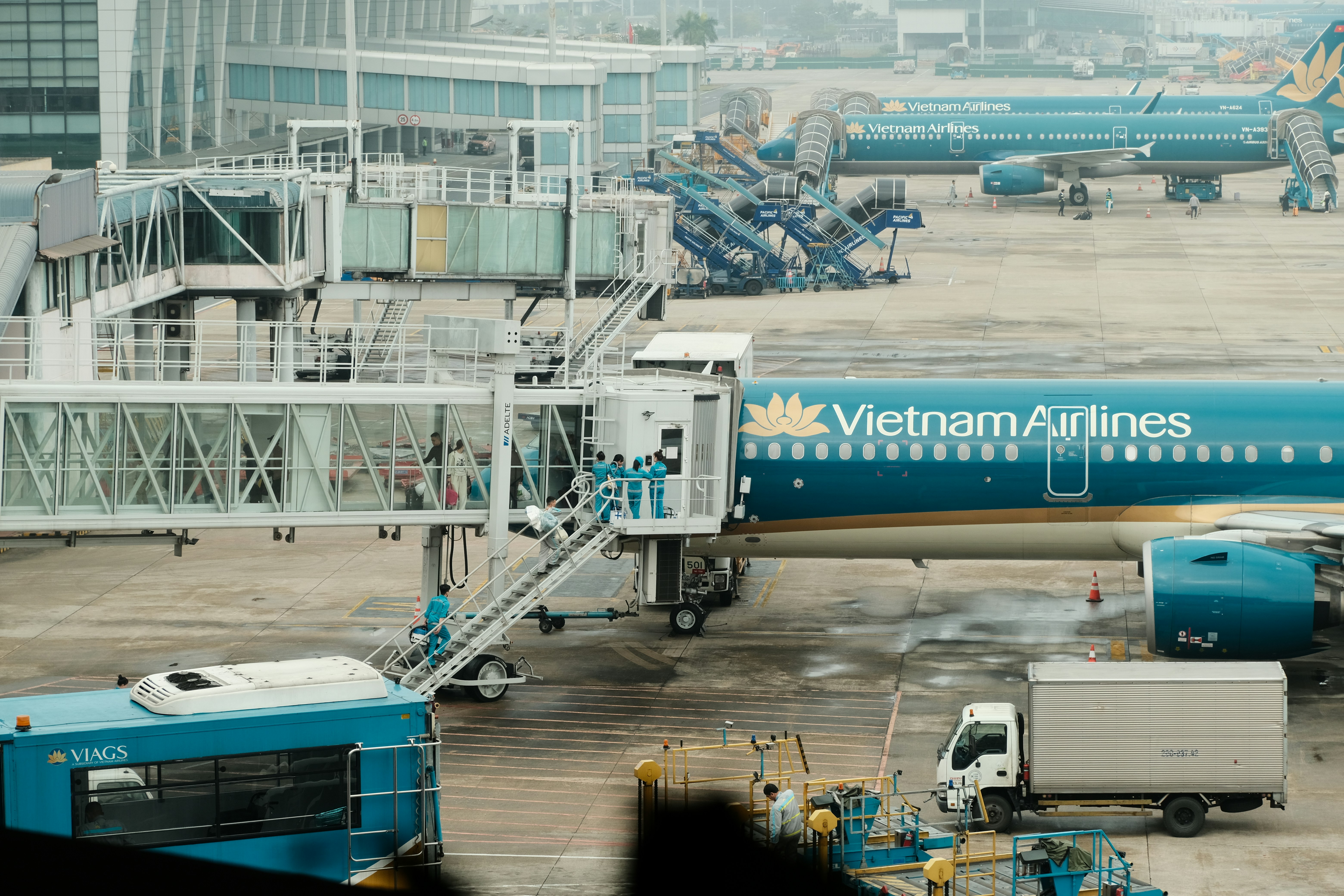 Vietnam Airlines plane docked at an airport gate with service vehicles and crew preparing for departure.
