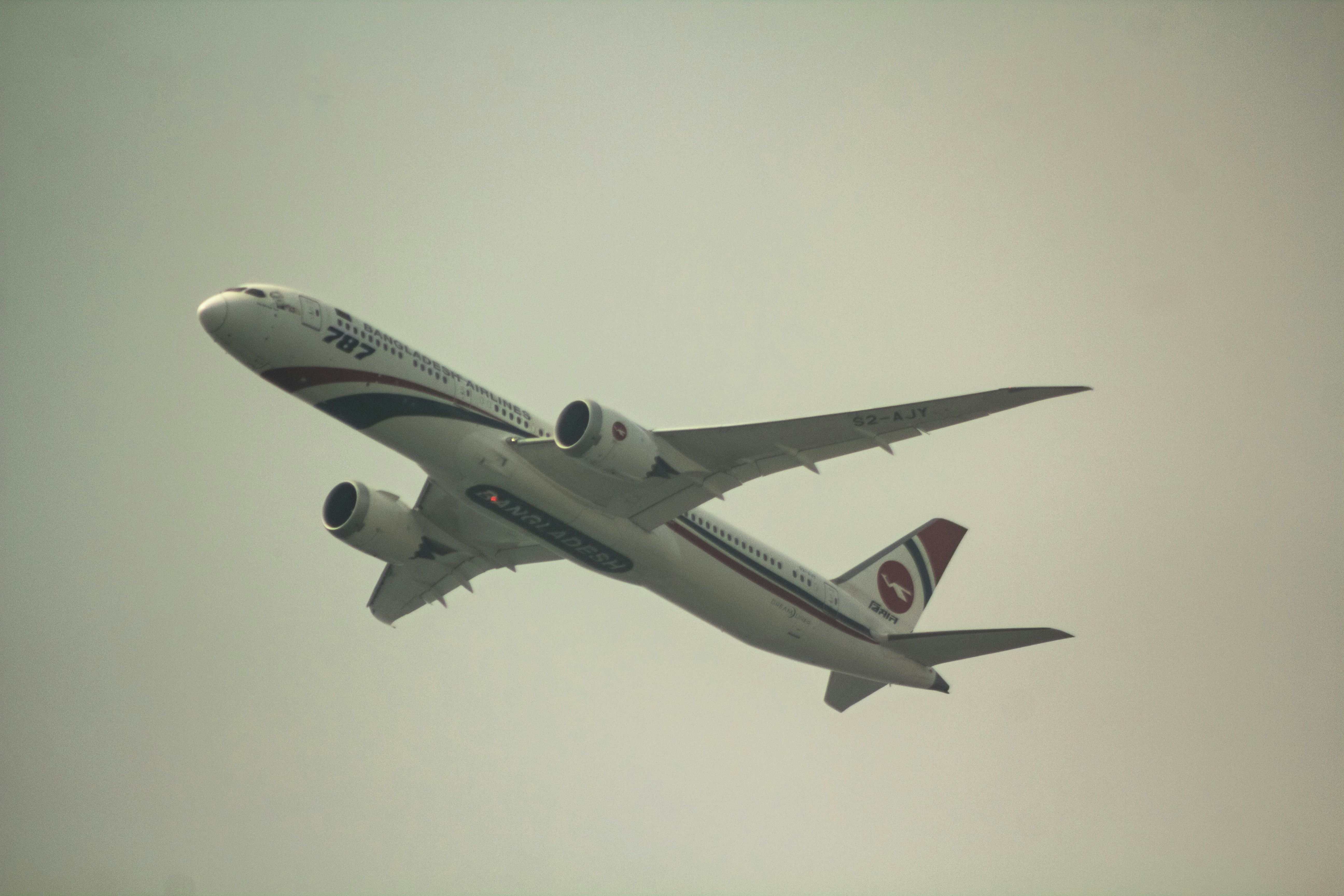 Takeoff under a muted sky: a distant view of a white jet with red tail lifting off