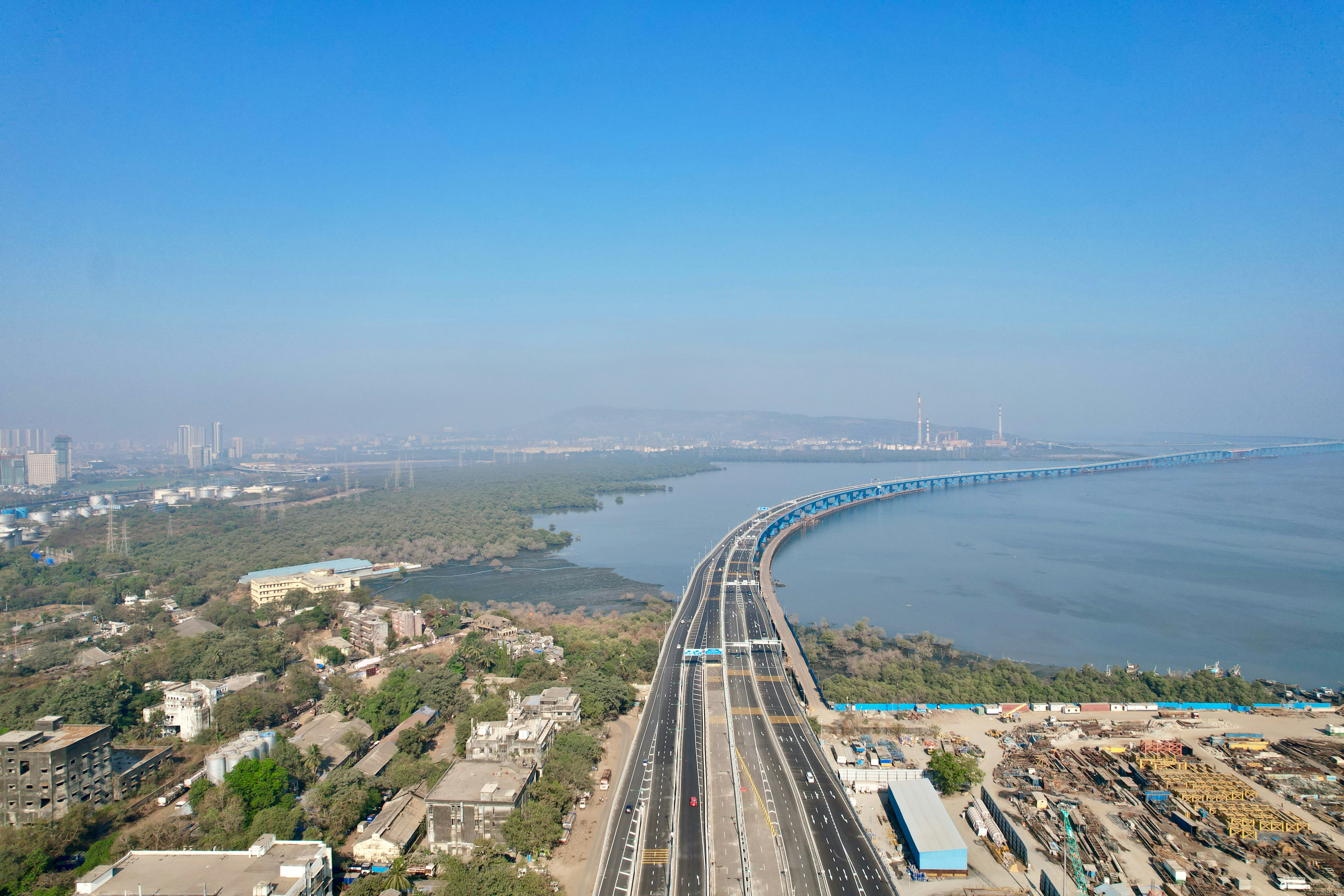 Aerial view showcasing a highway bridge gracefully arching over a serene waterway, juxtaposed with urban landscapes and greenery.