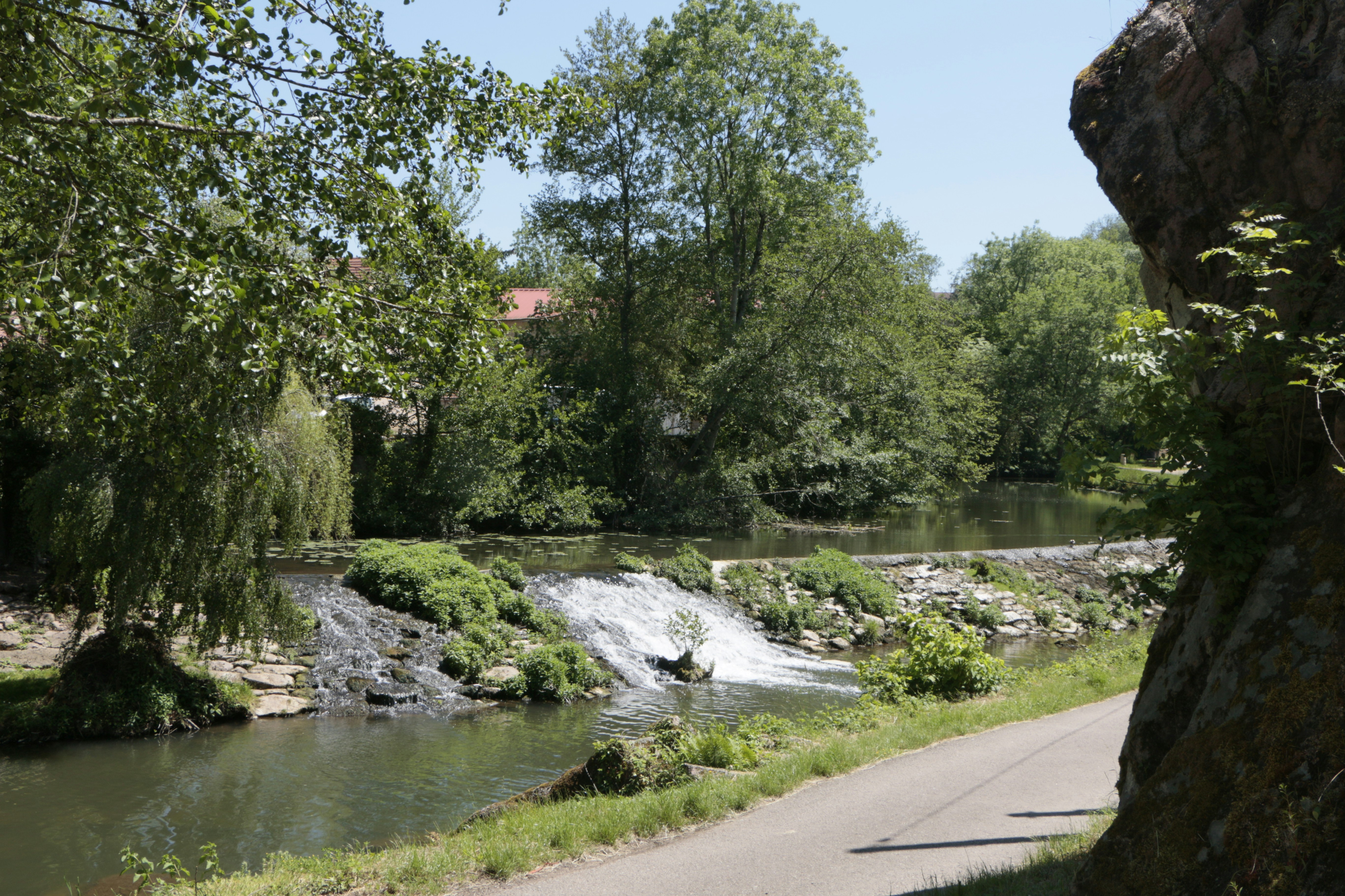 Tranquil river flowing past lush greenery and a cascading waterfall under a clear sky.