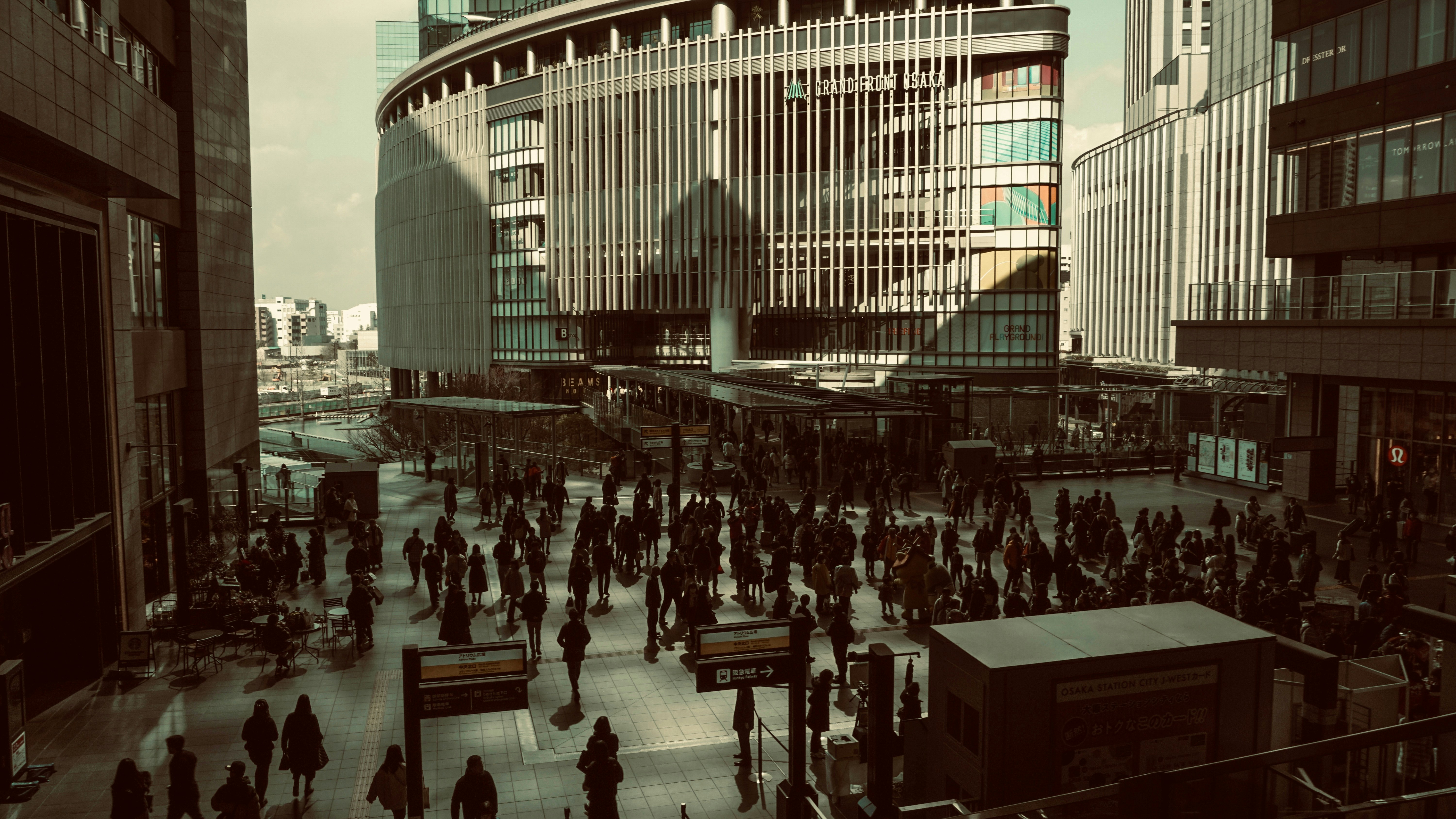 Pulse at the Glass Arc: Pedestrians Converge in a Sepia City Plaza