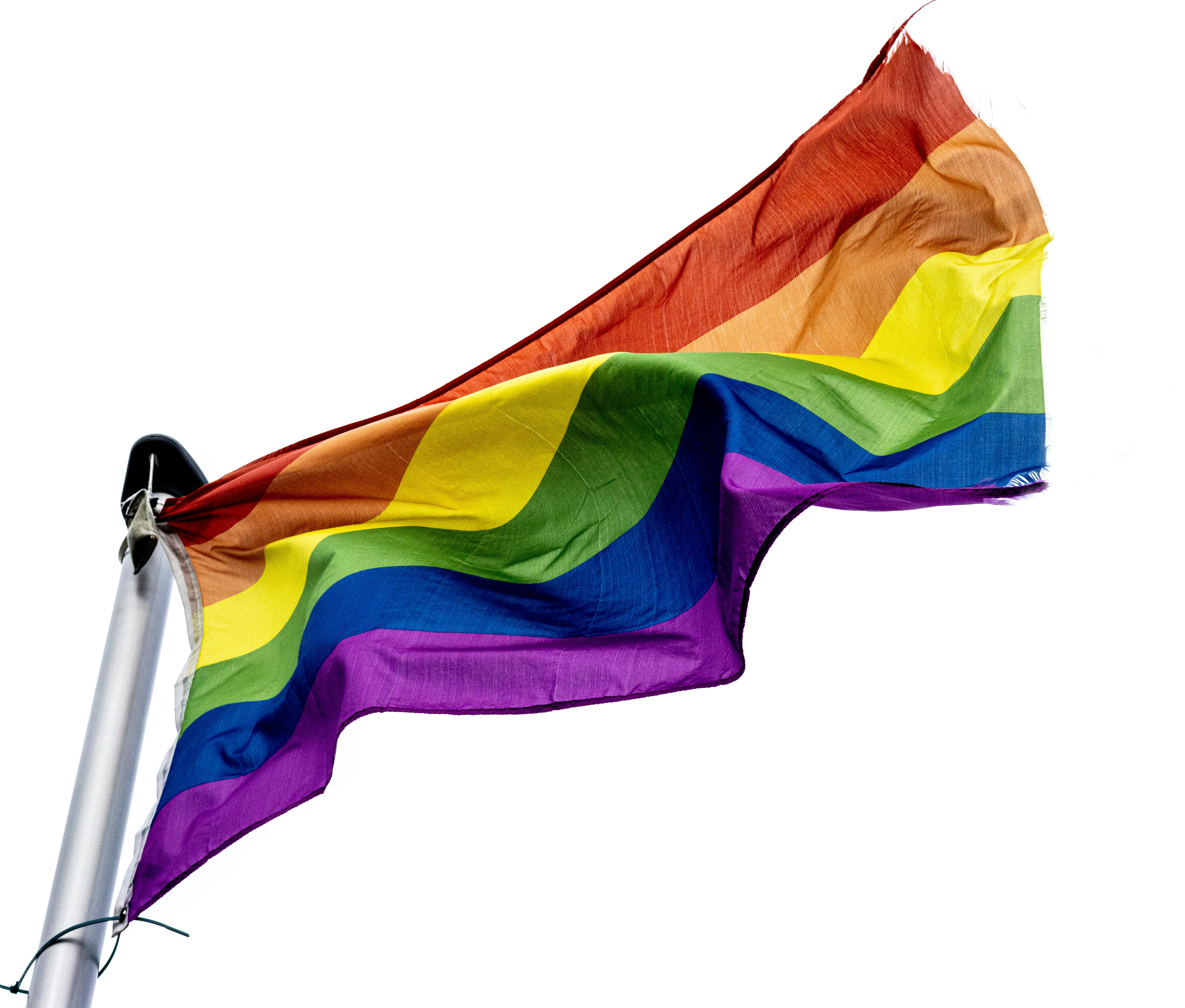 Vibrant Pride flag unfurling against a clear sky, symbolizing diversity and acceptance.
