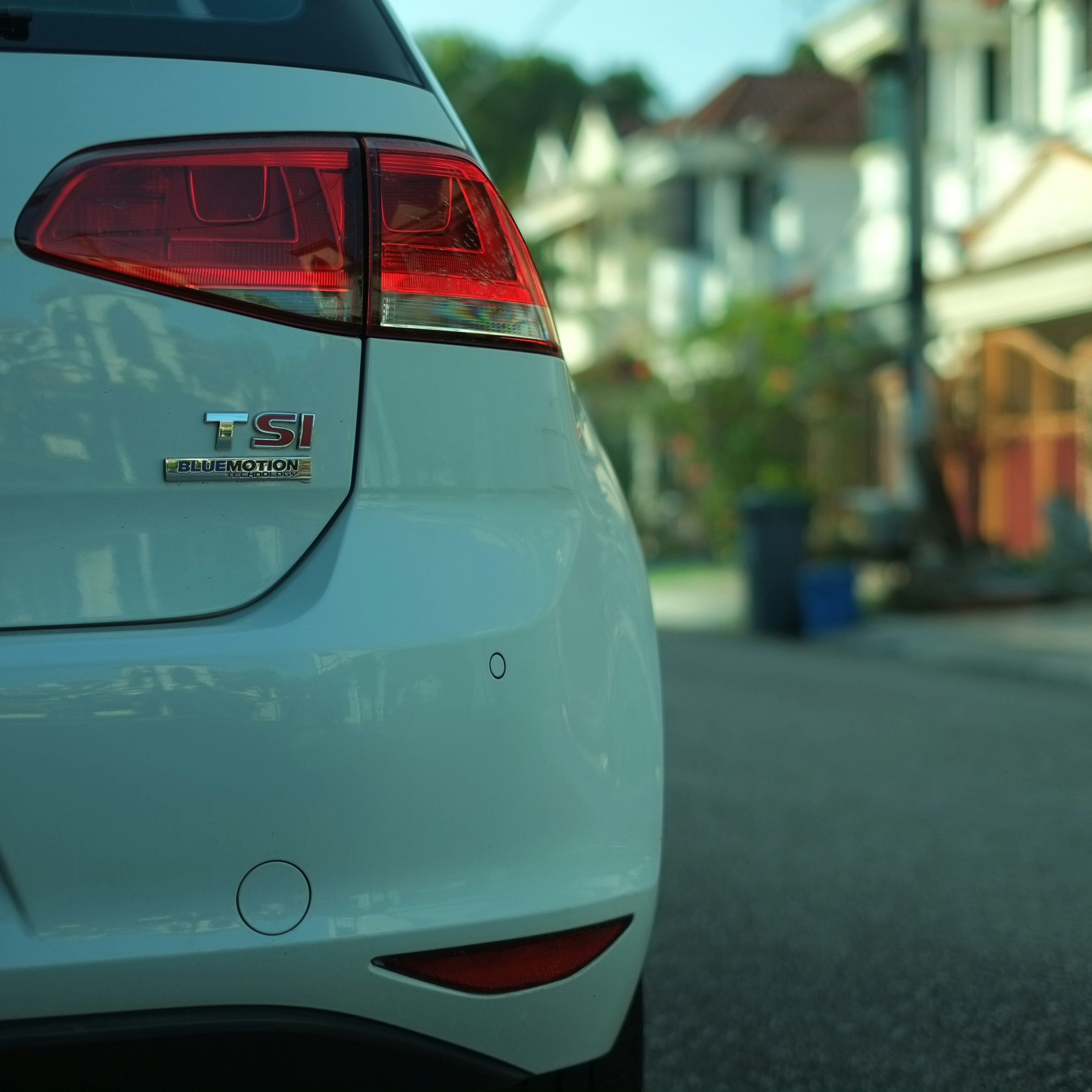BlueMotion Emblem in Quiet Suburban Frame: White VW Hatchback, Tail Light in Focus