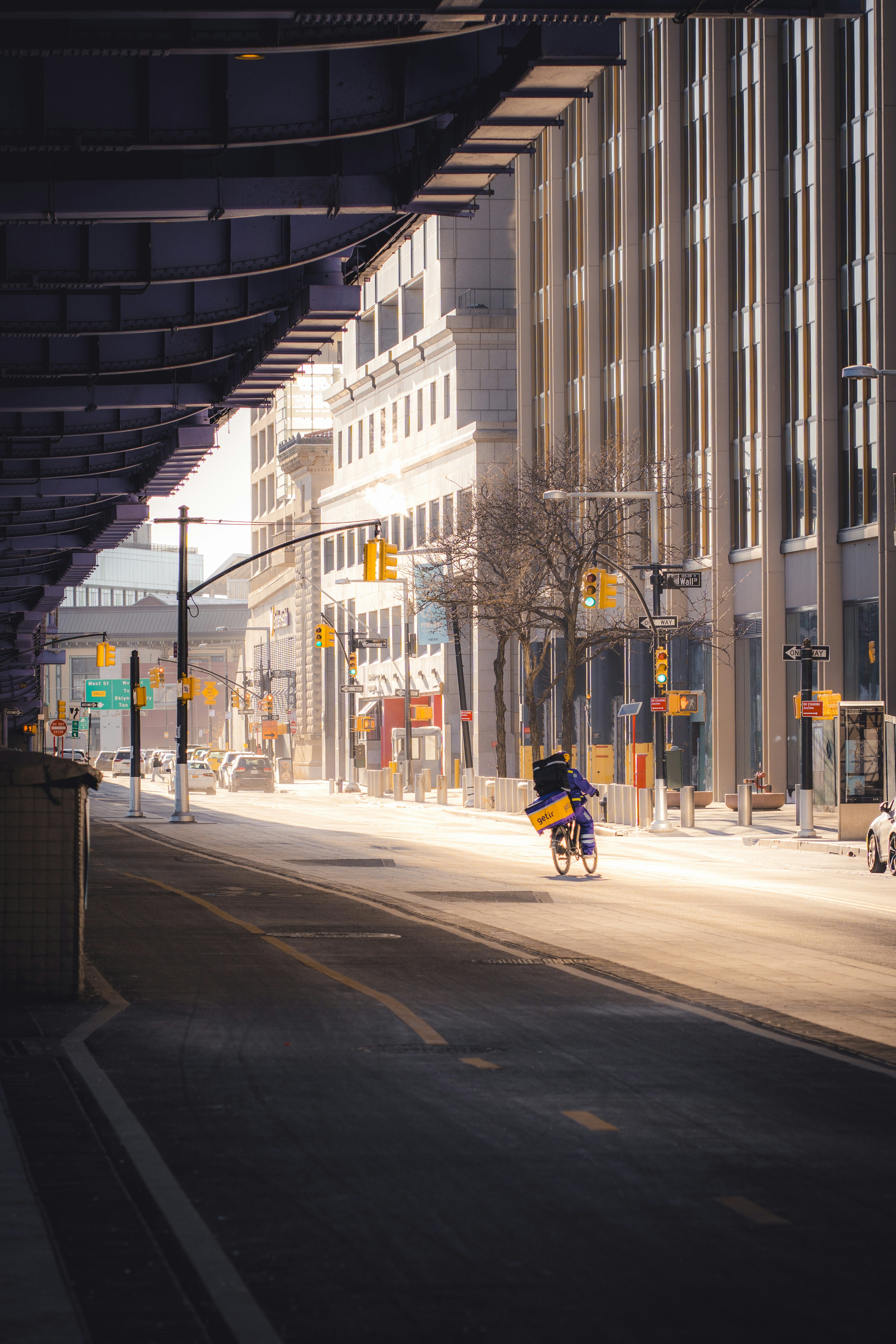 Sunlit Transit Corridor: A Cyclist Traverses a Quiet City Street Under a Raised Highway