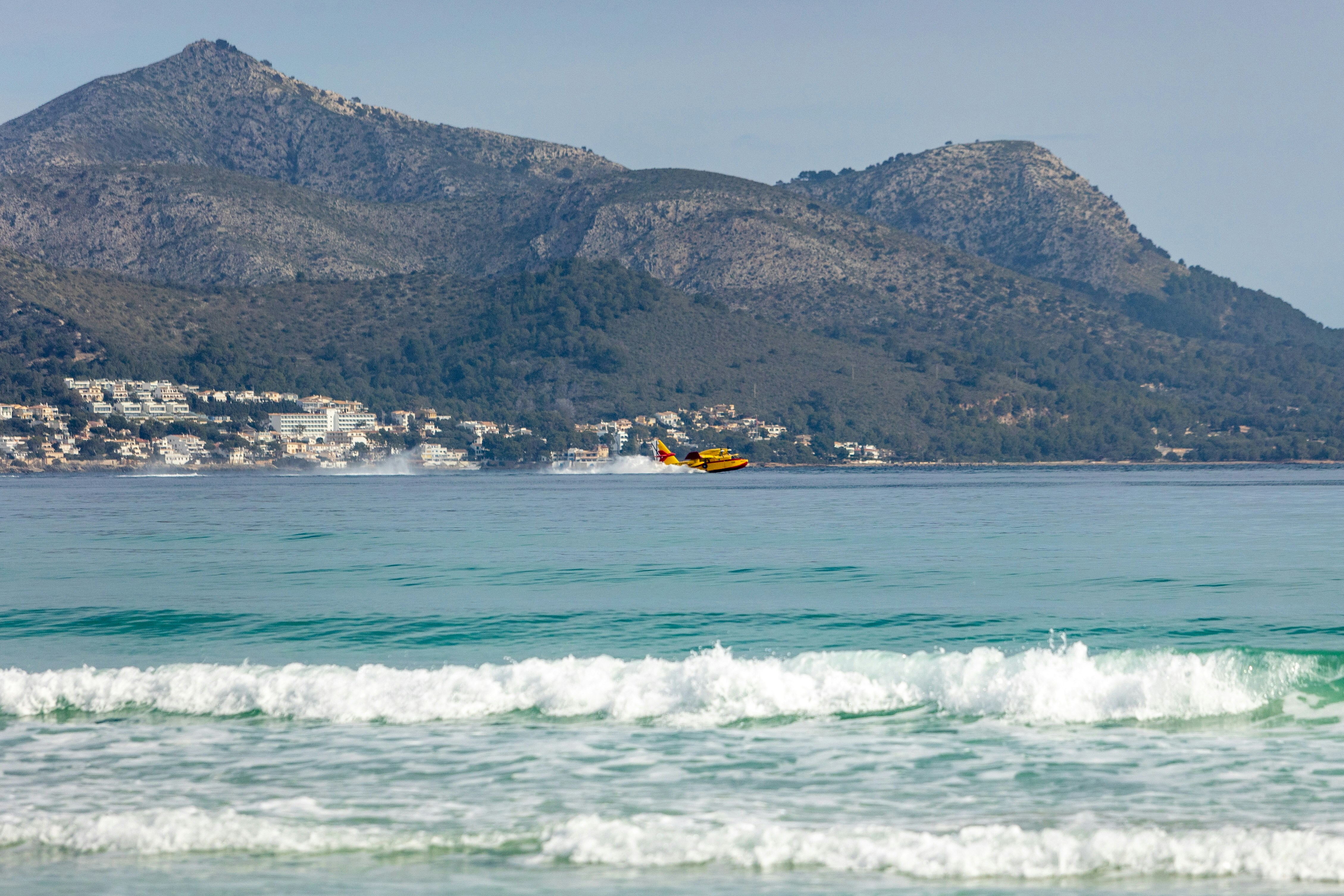 Yellow seaplane skimming ocean surface near Mallorca with mountains in the background.
