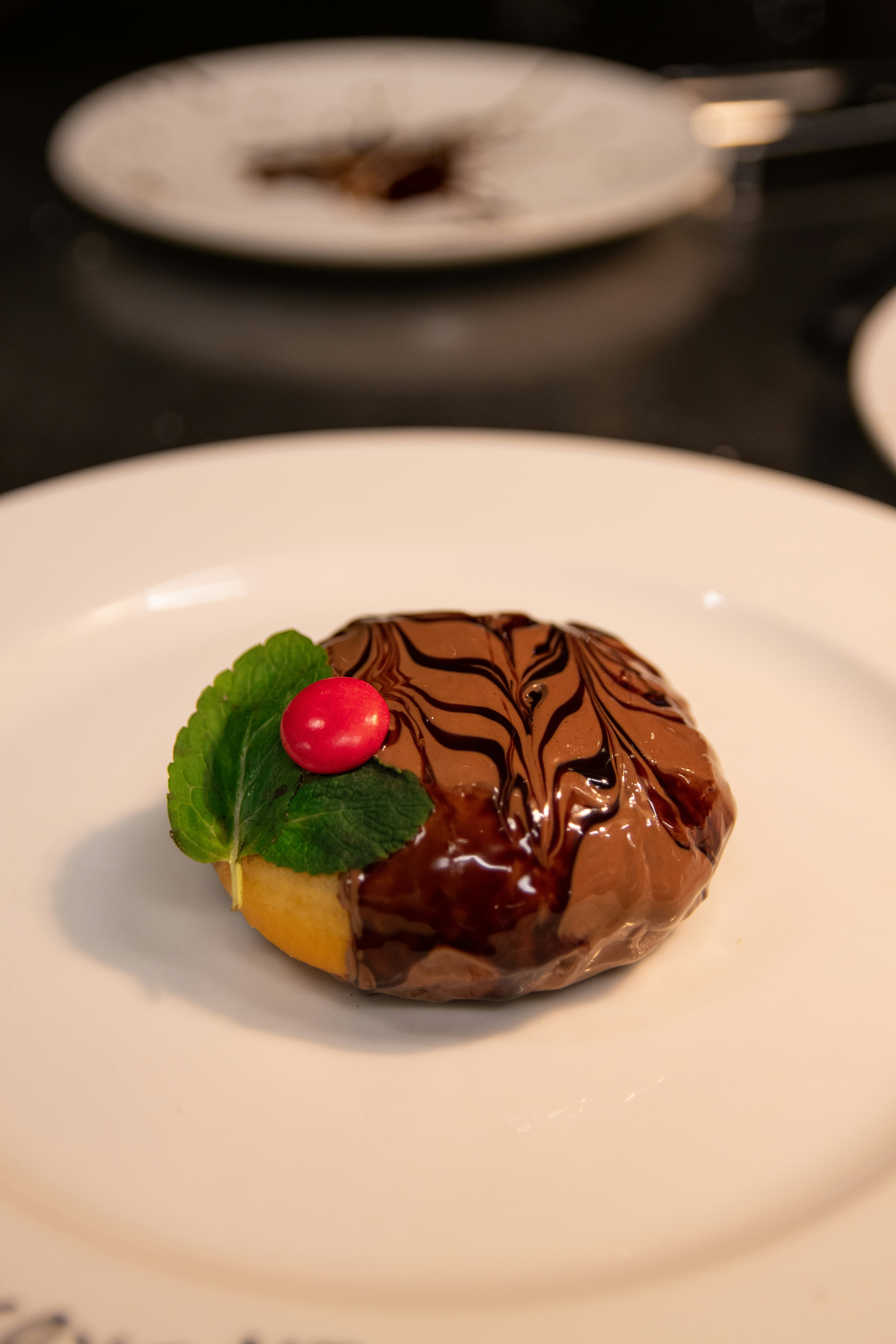 Glossy Chocolate-glazed Donut on a White Plate with Mint Garnish